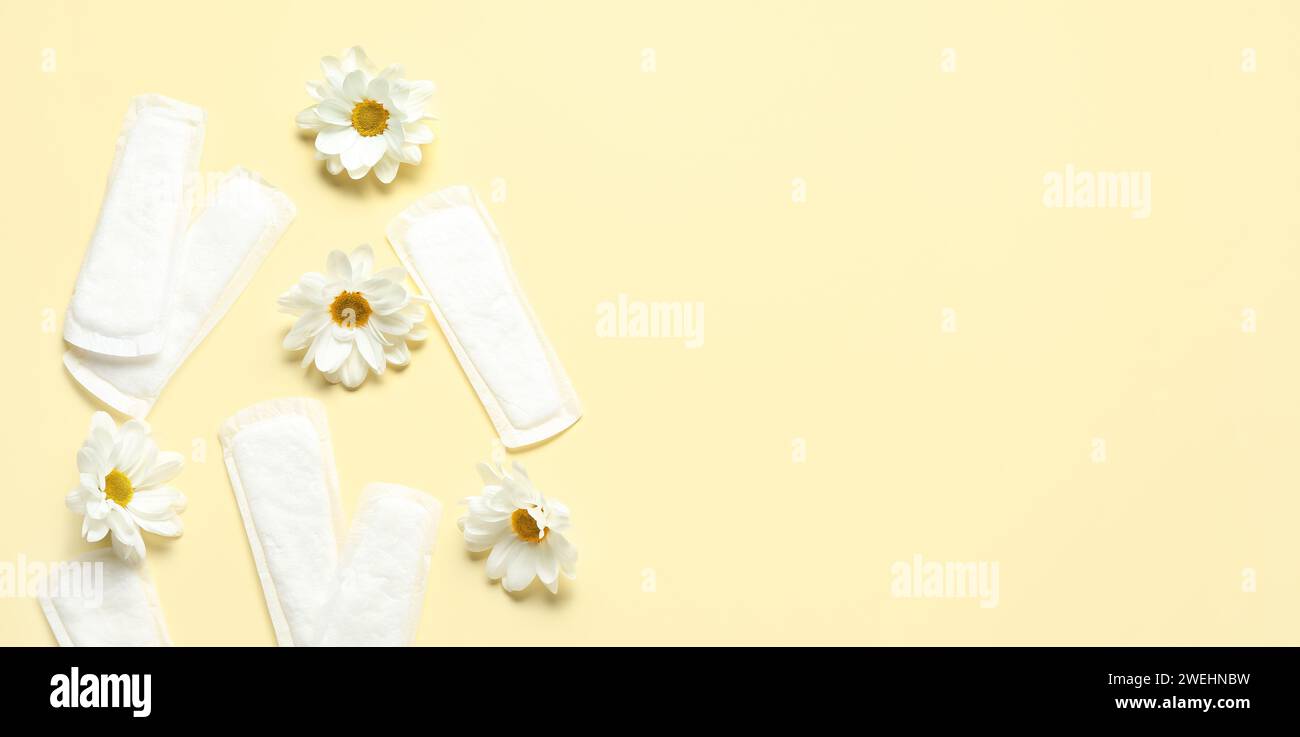 Menstrual pads and beautiful chamomile flowers on light yellow ...
