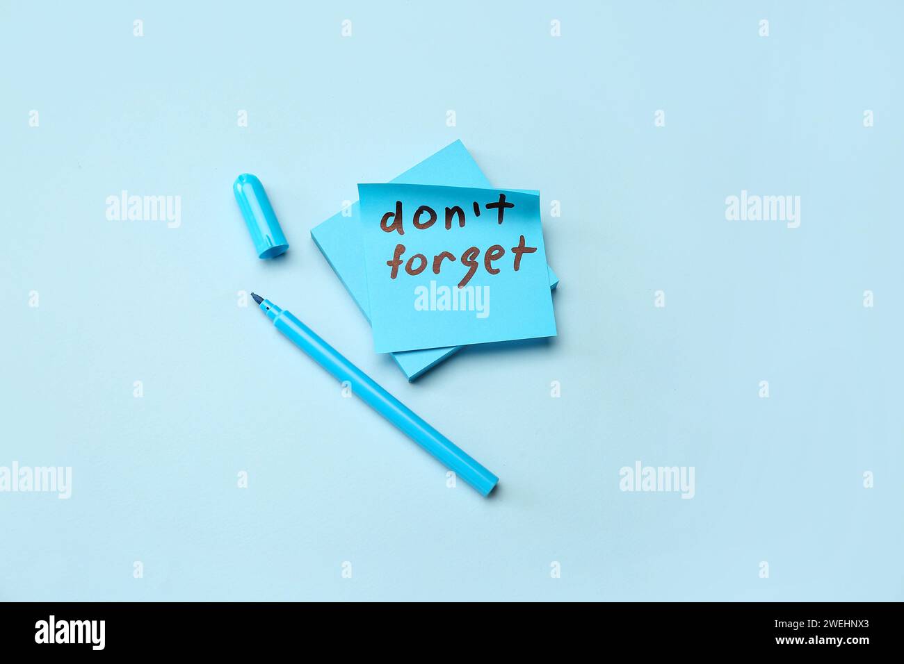 Sticky note with text DON'T FORGET and felt-tip pen on blue background ...