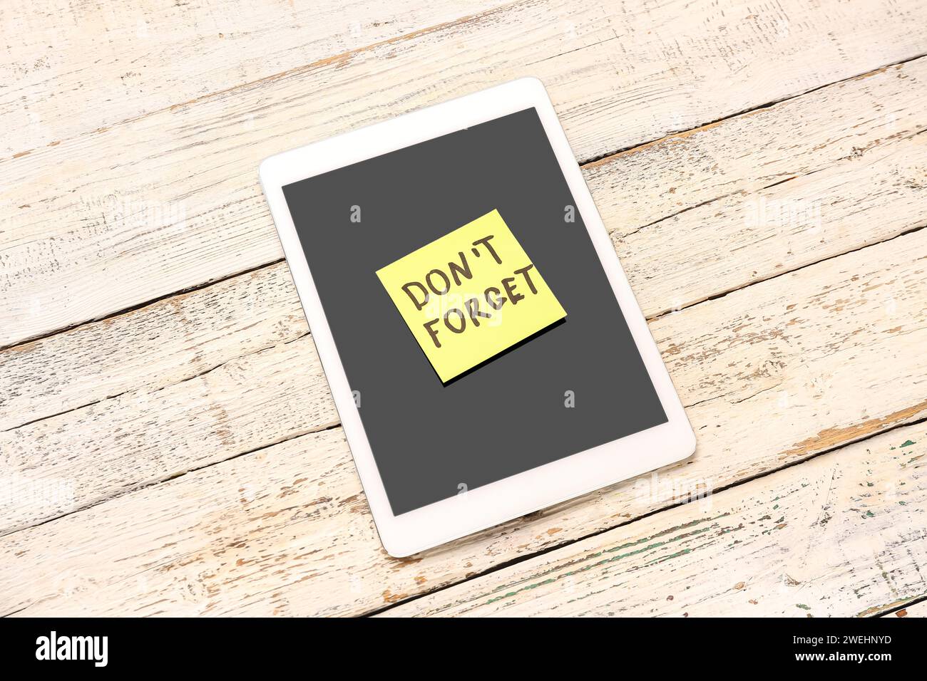 Sticky note with text DON'T FORGET and tablet computer on white wooden ...