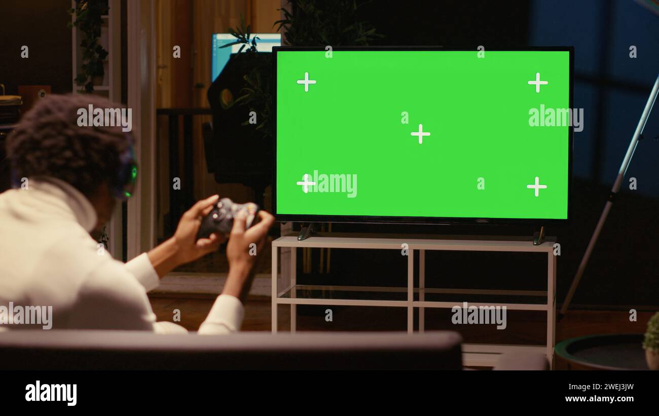 Man in dimly lit apartment playing video games on green screen ...