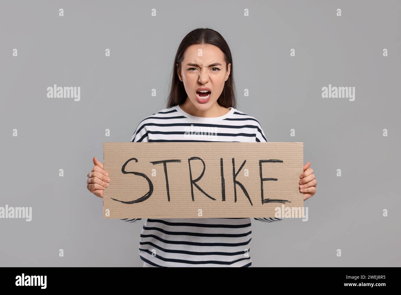 Angry young woman holding cardboard banner with word Strike on light ...