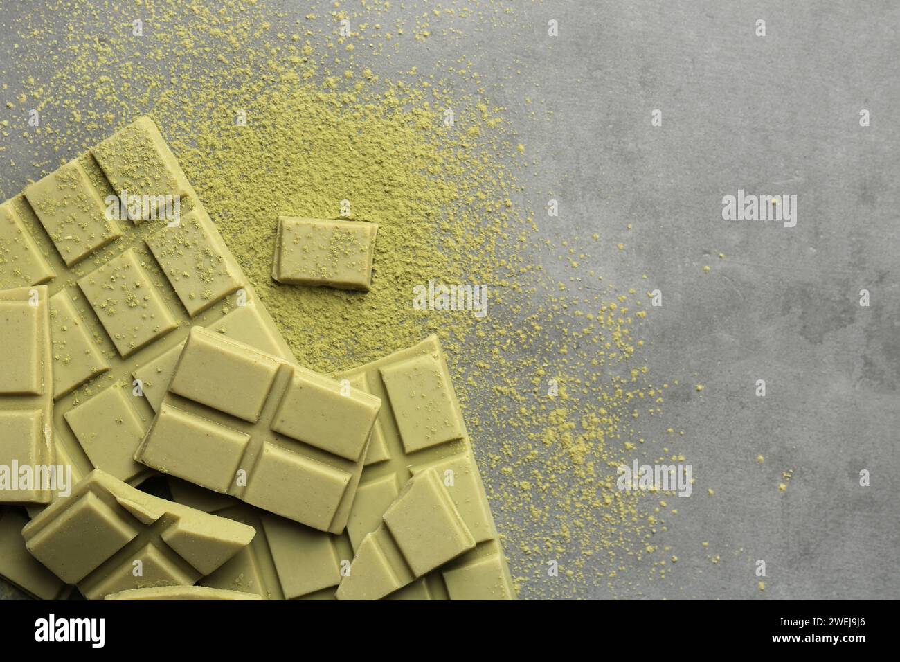 Pieces of tasty matcha chocolate bars and powder on grey textured table ...
