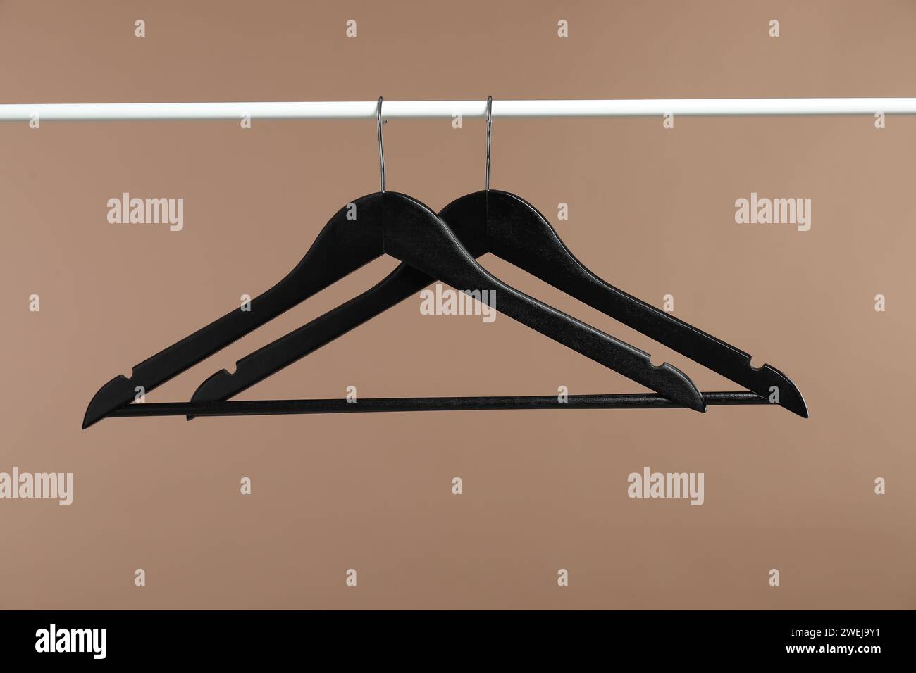 Black clothes hangers on rack against light brown background Stock ...