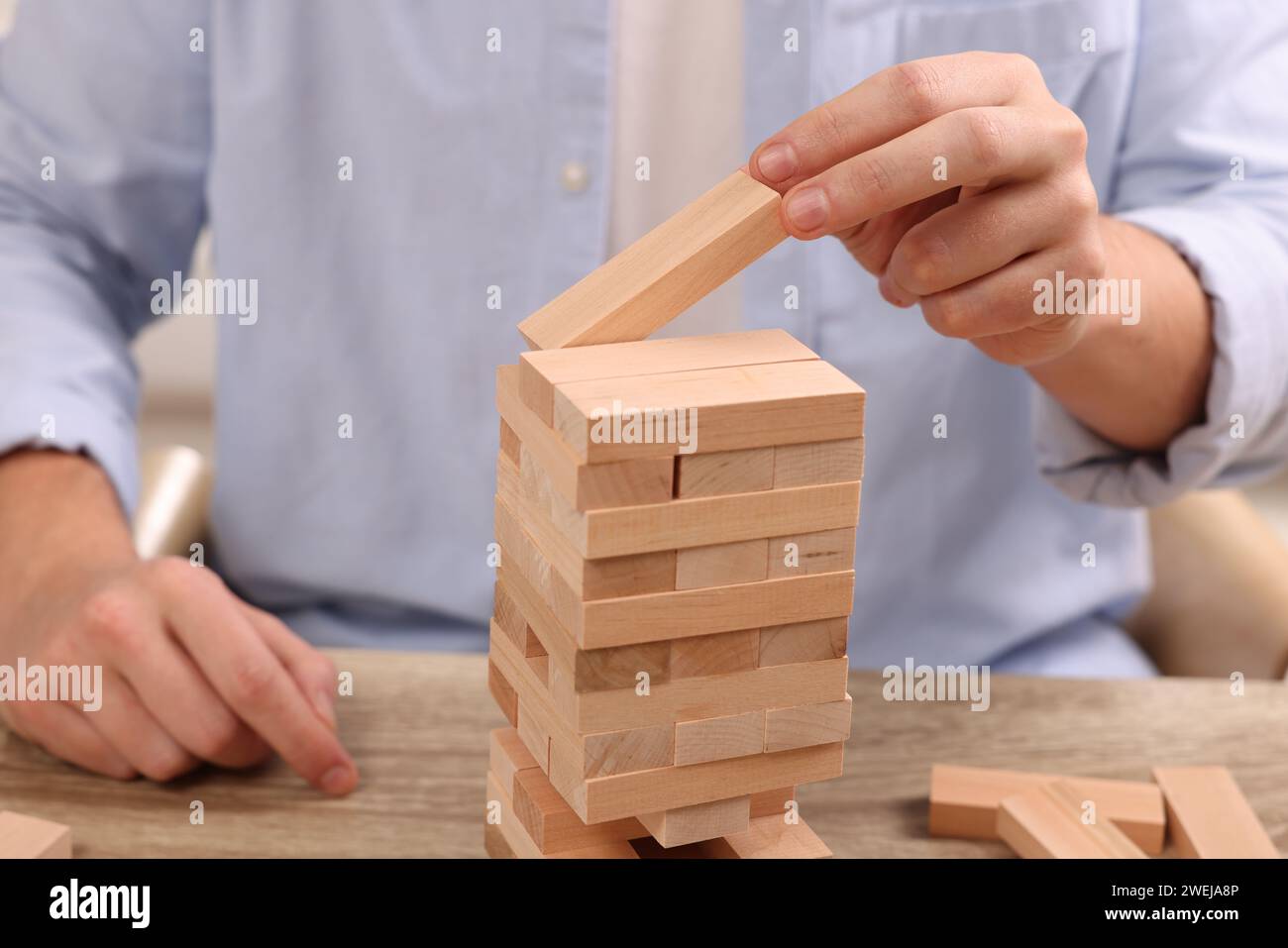 Playing Jenga. Man building tower with wooden blocks at table, closeup ...