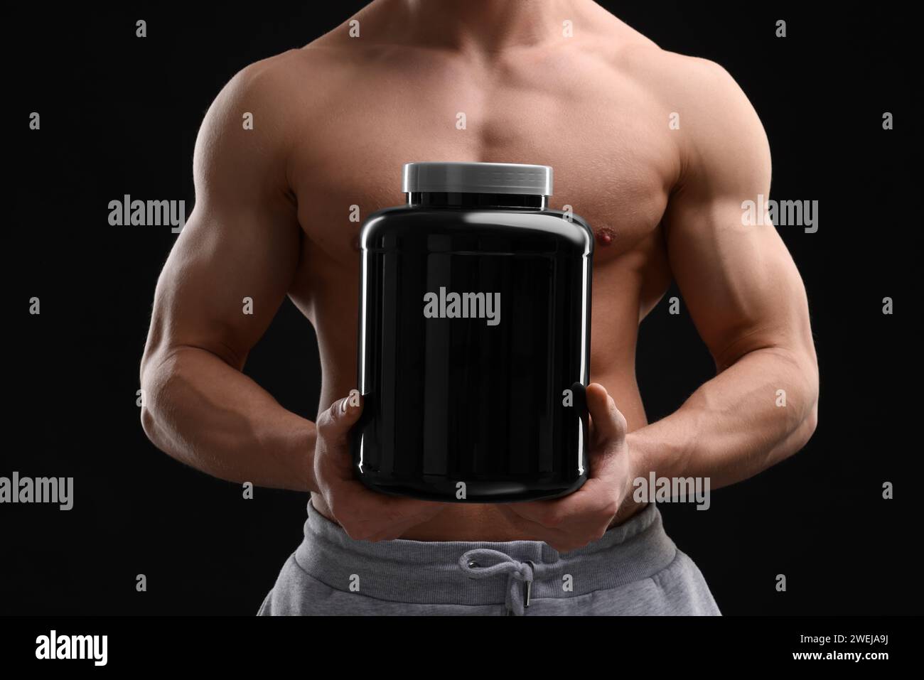 Young man with muscular body holding jar of protein powder on black ...