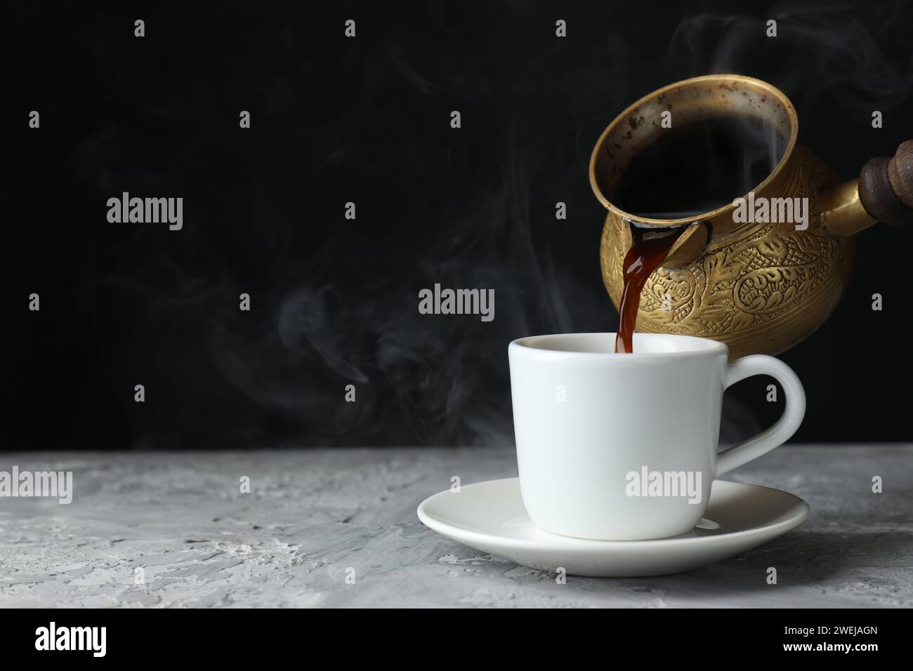 Turkish coffee. Pouring brewed beverage from cezve into cup at grey ...