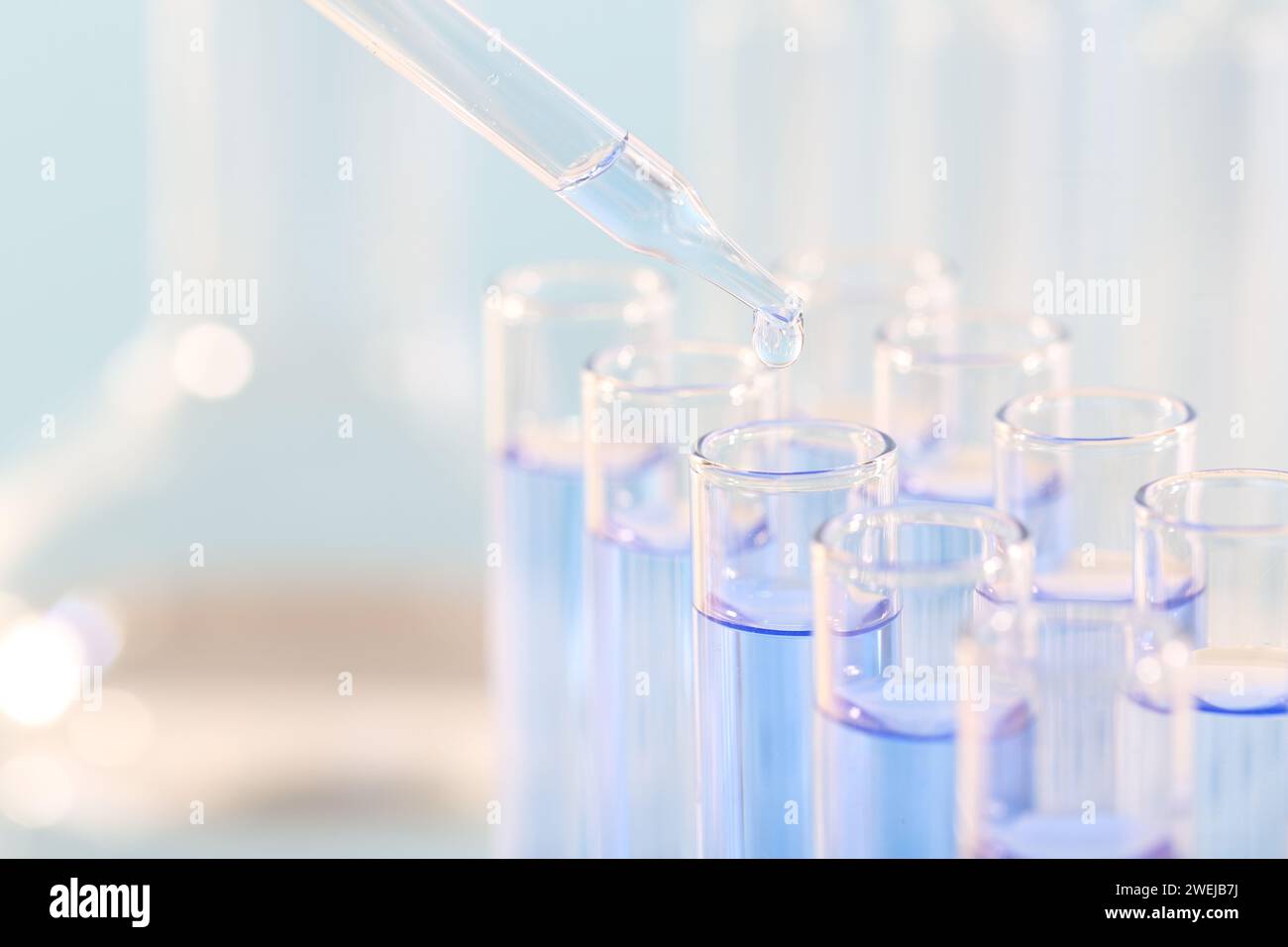 Laboratory analysis. Dripping light blue liquid from pipette into glass ...