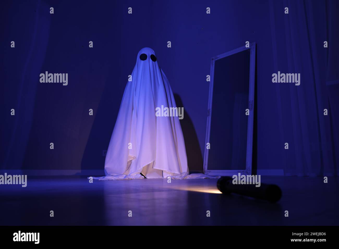 Creepy ghost. Woman covered with sheet in blue light, low angle view ...