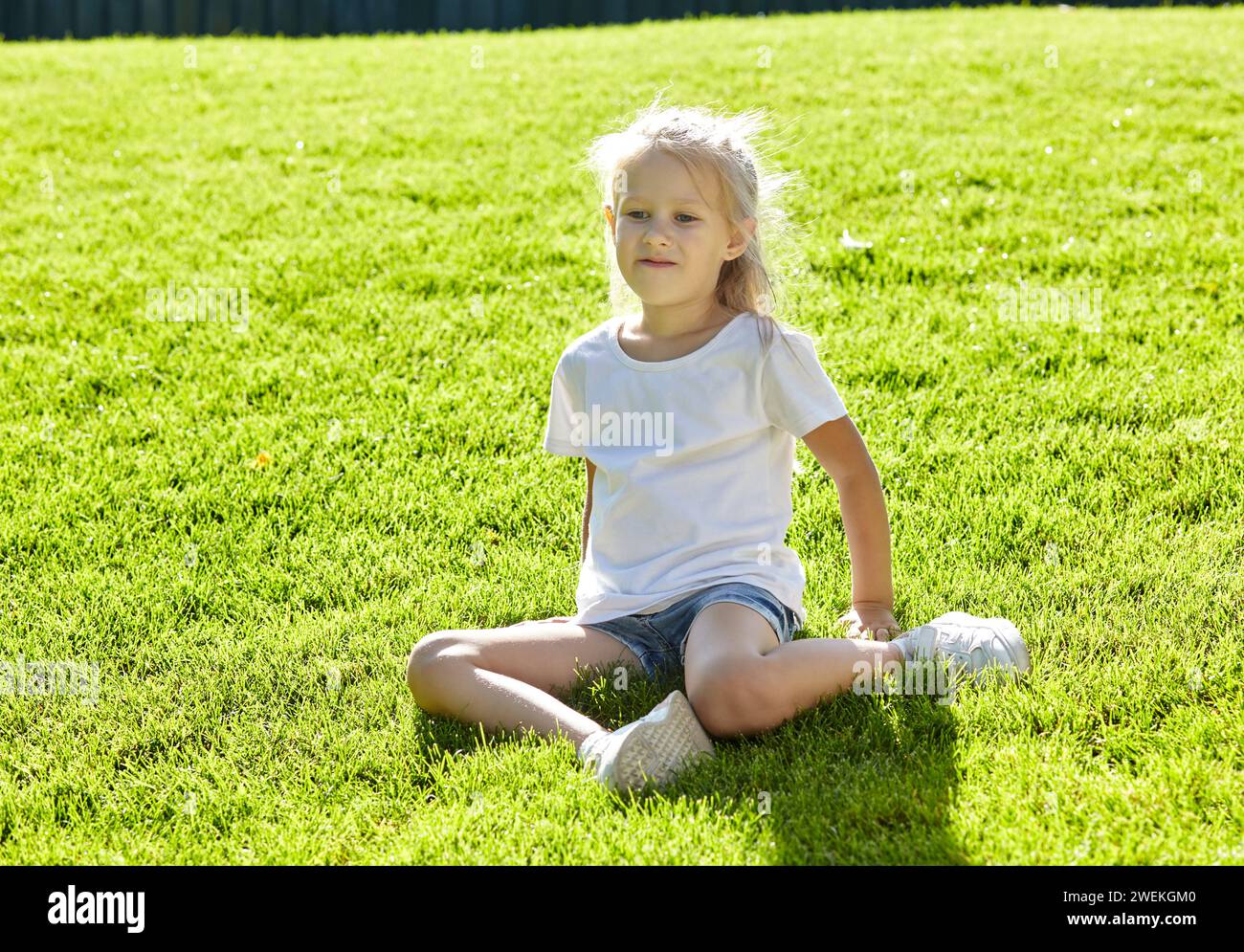 Little girl sitting on the lawn in the summer city park. Childhood ...