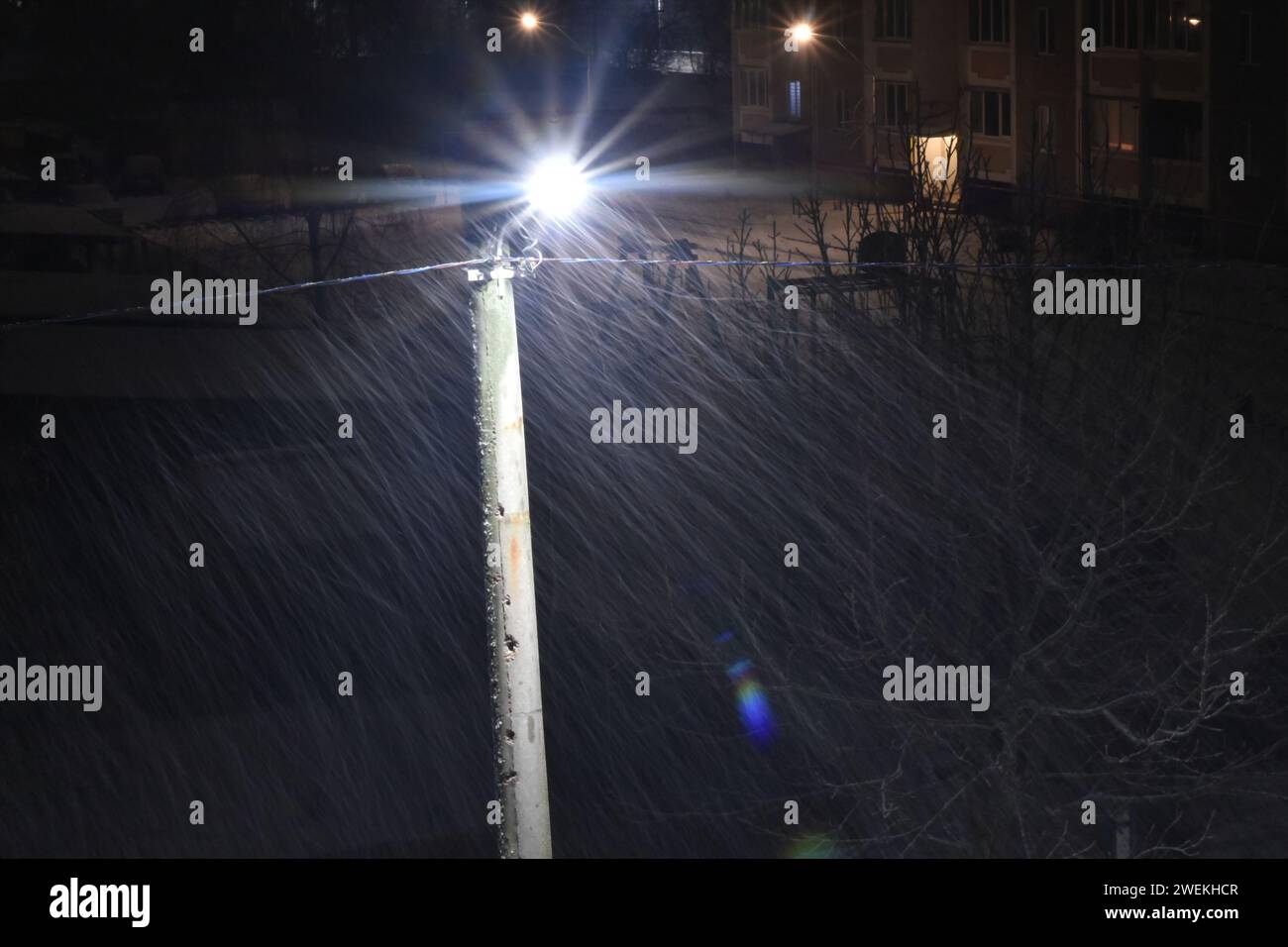 In the light of a street lamp, falling snow is visible, driven by the ...