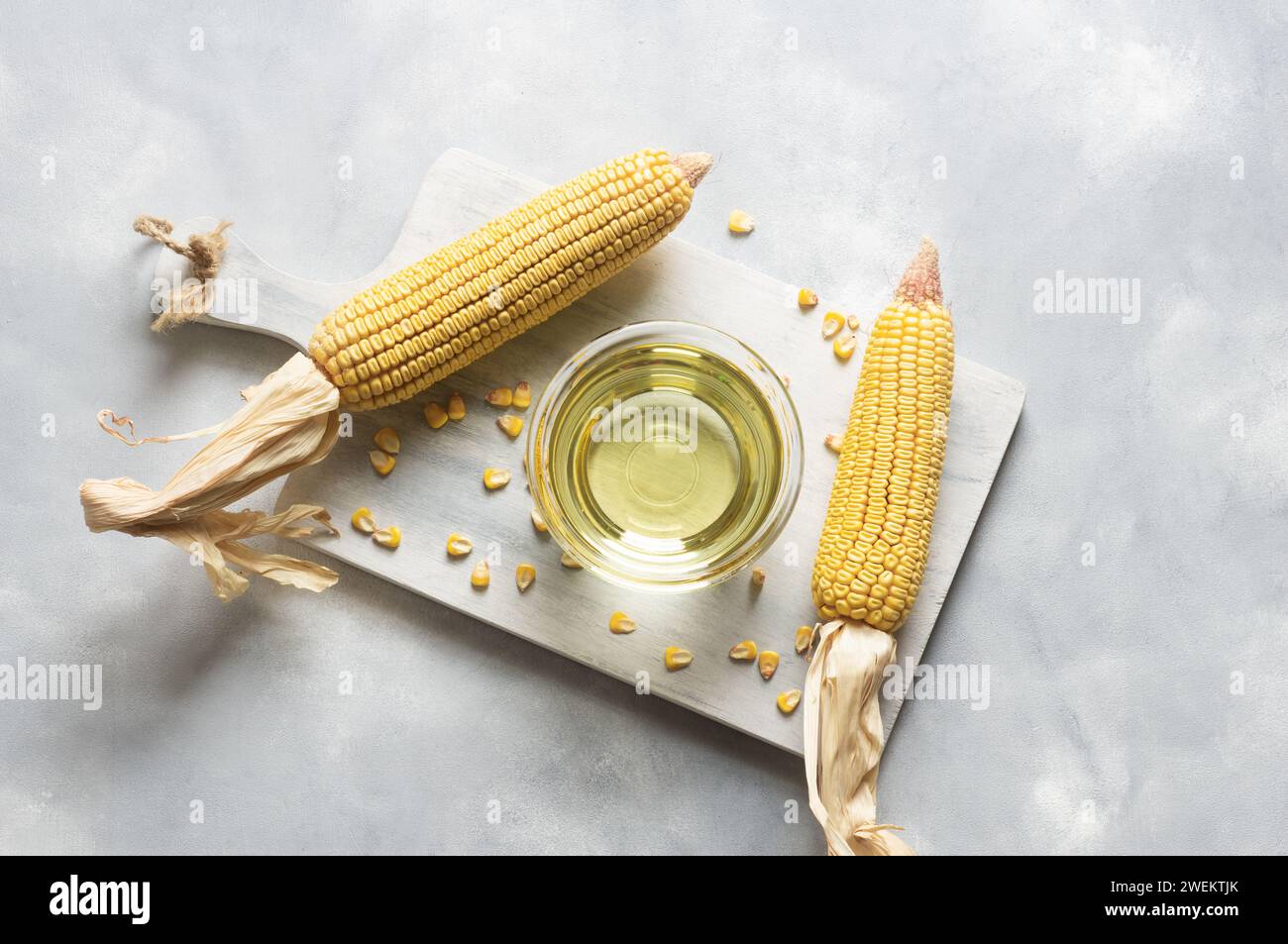 Corn oil in bowl with dried corn groats and kernels on rustic backdrop ...