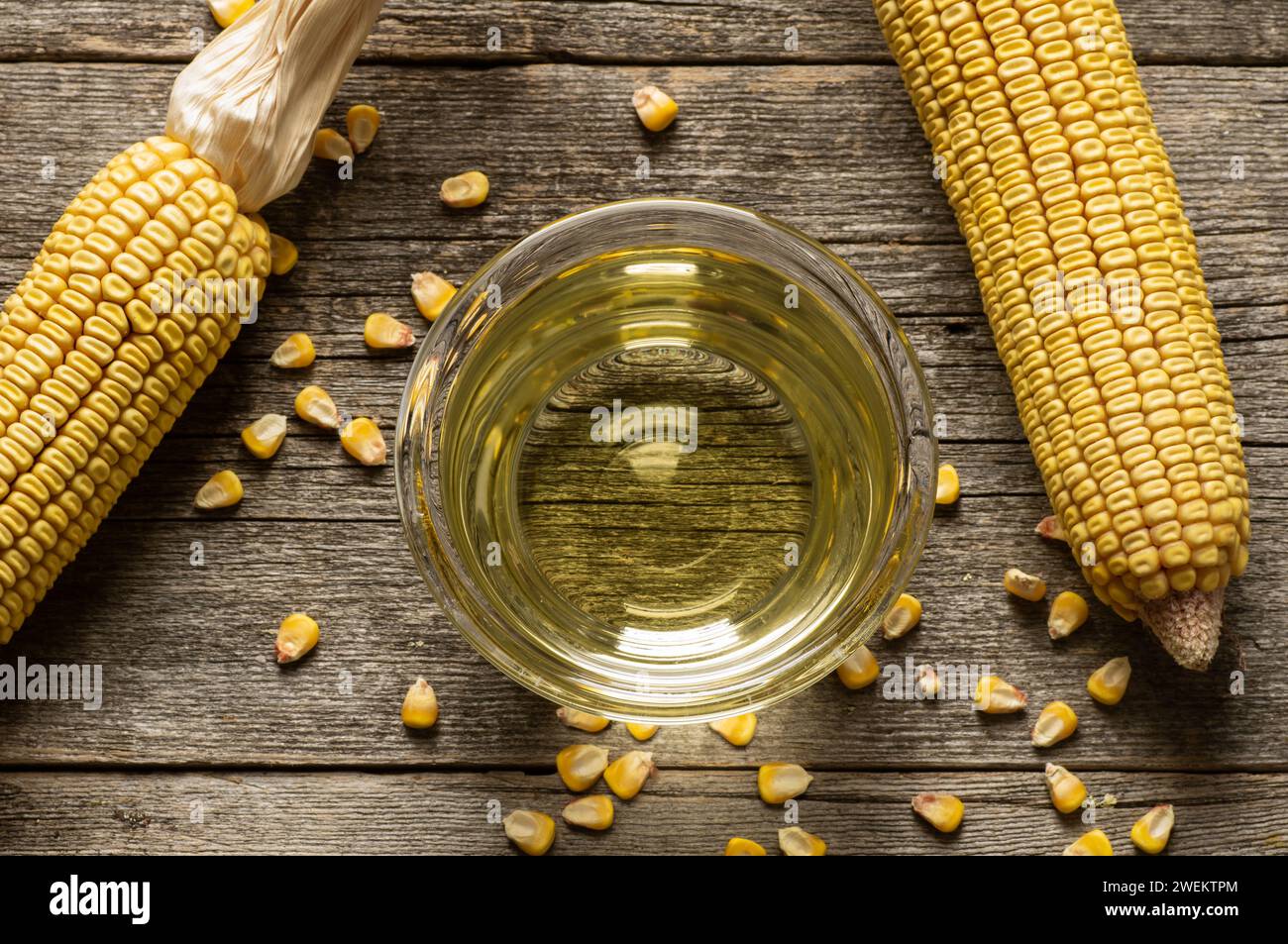 Corn oil in bowl with dried corn groats and kernels on rustic backdrop ...