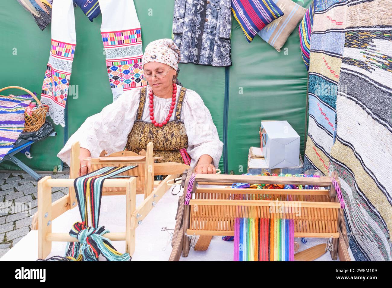 Senior white woman at pavilion of traditional Irbit fair weaving ...
