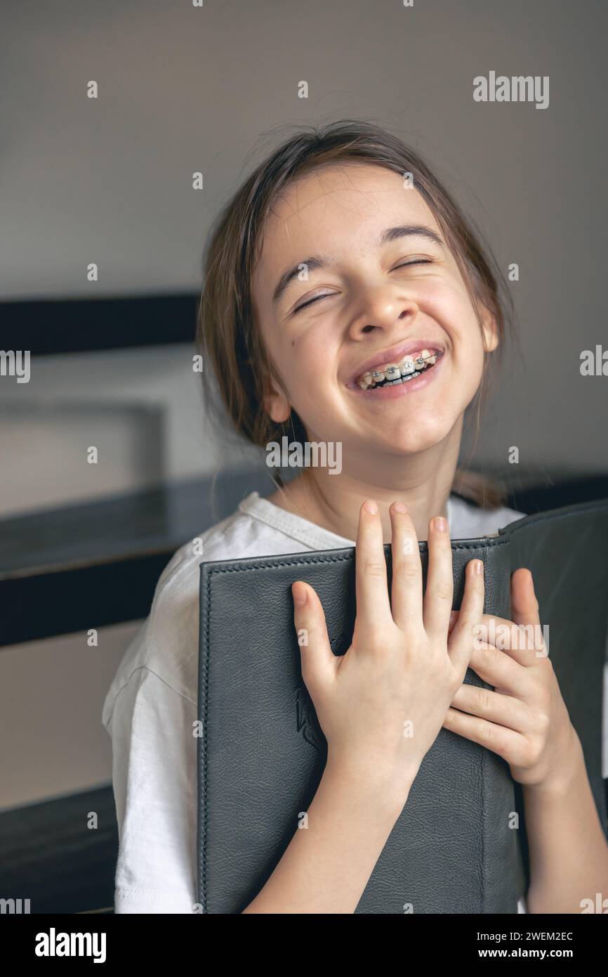 A teenage girl reads a book and smiles, showing her teeth with braces ...