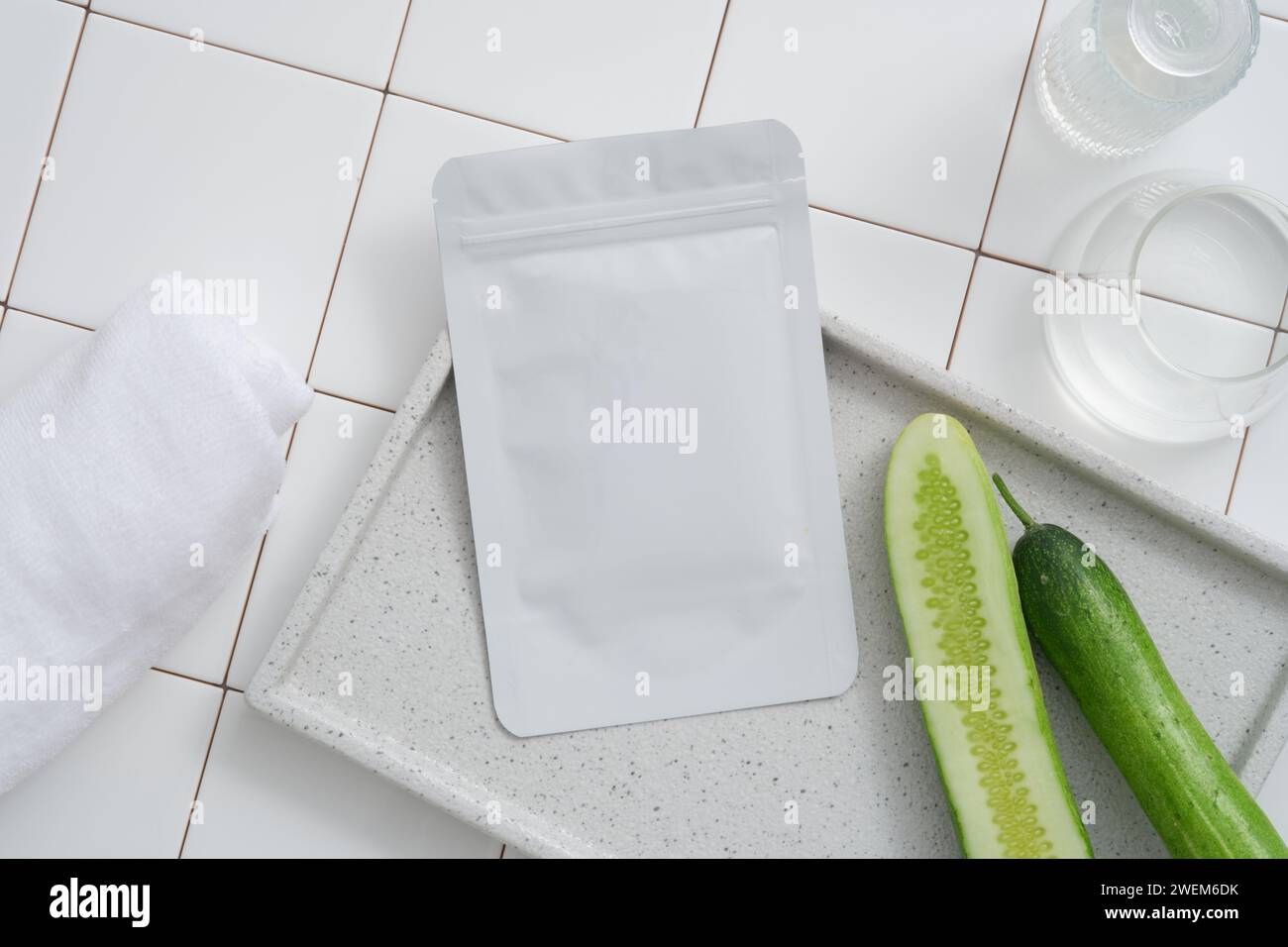 Facial sheet mask packaging mockup with fresh cucumber, towel and glass ...