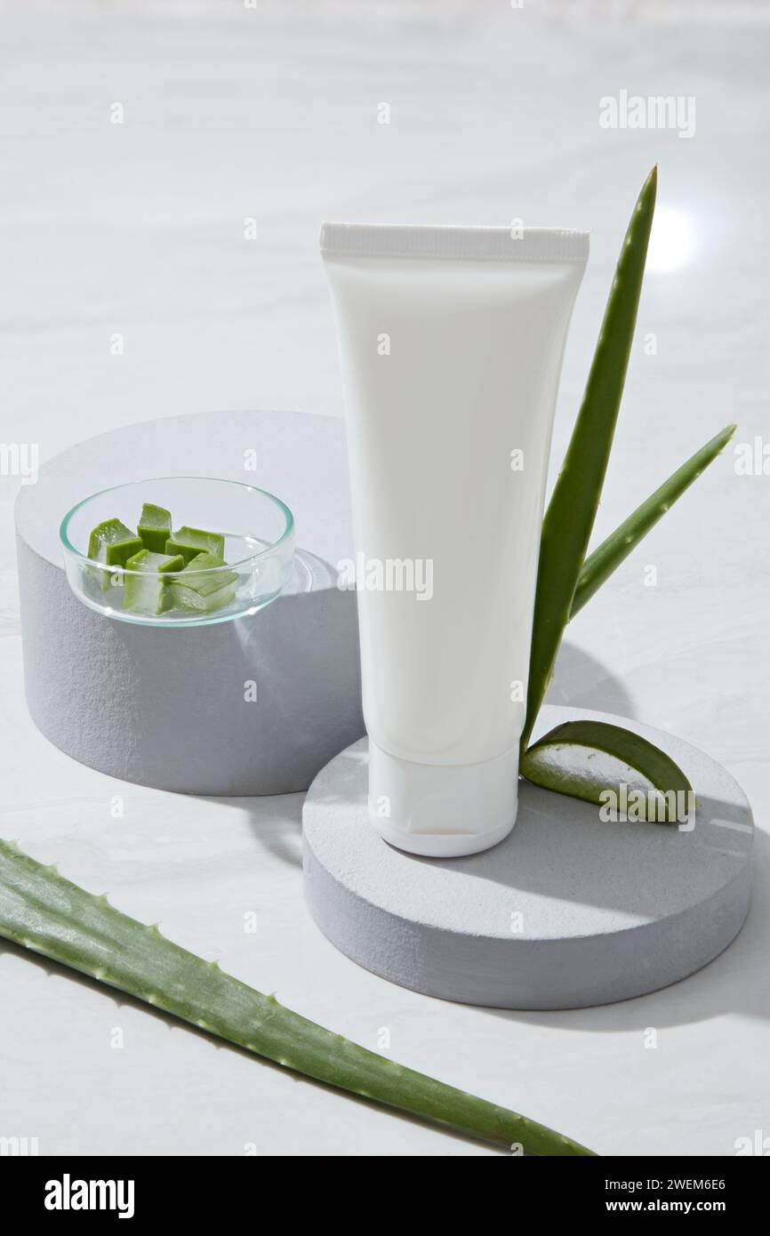 A white plastic tube unlabeled on round podium, fresh aloe vera on ...