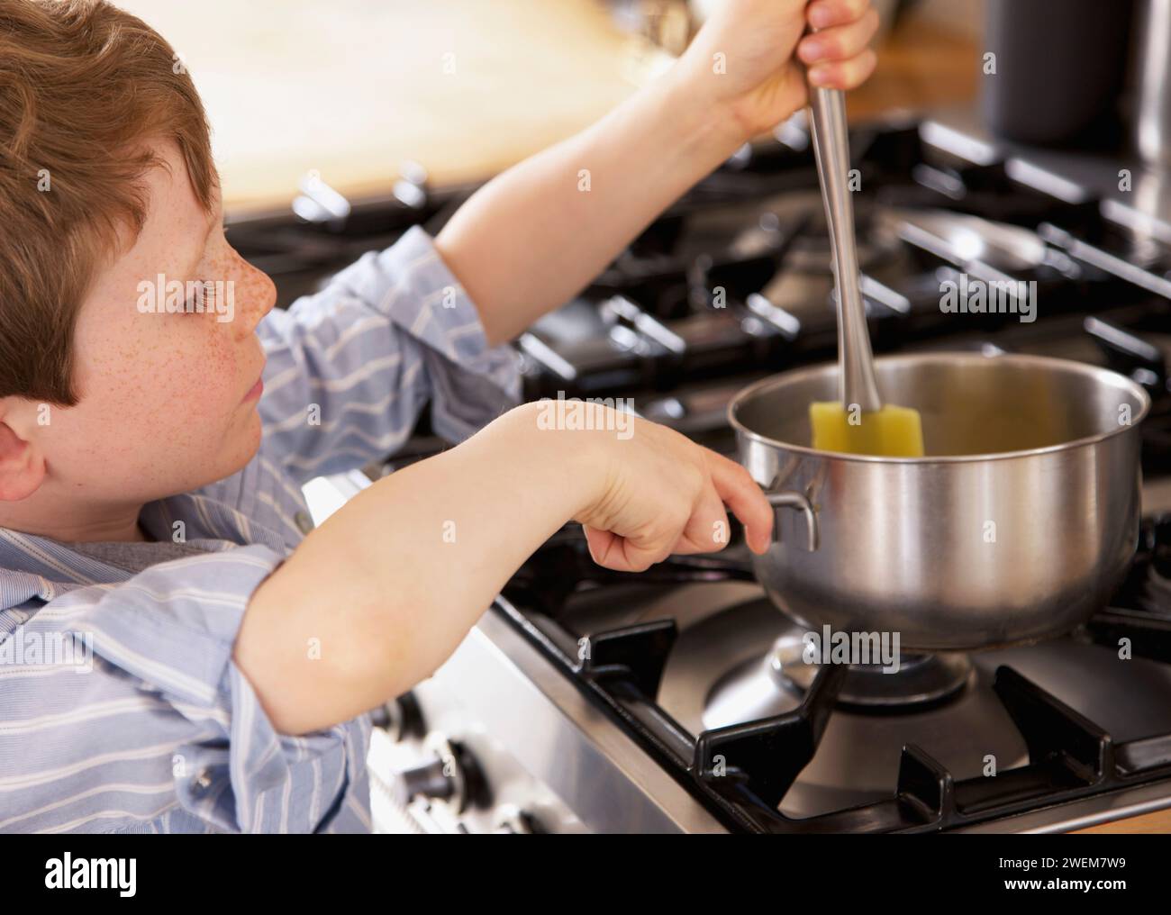 Young boy stirring and holding a saucepan over a cooker Stock Photo - Alamy