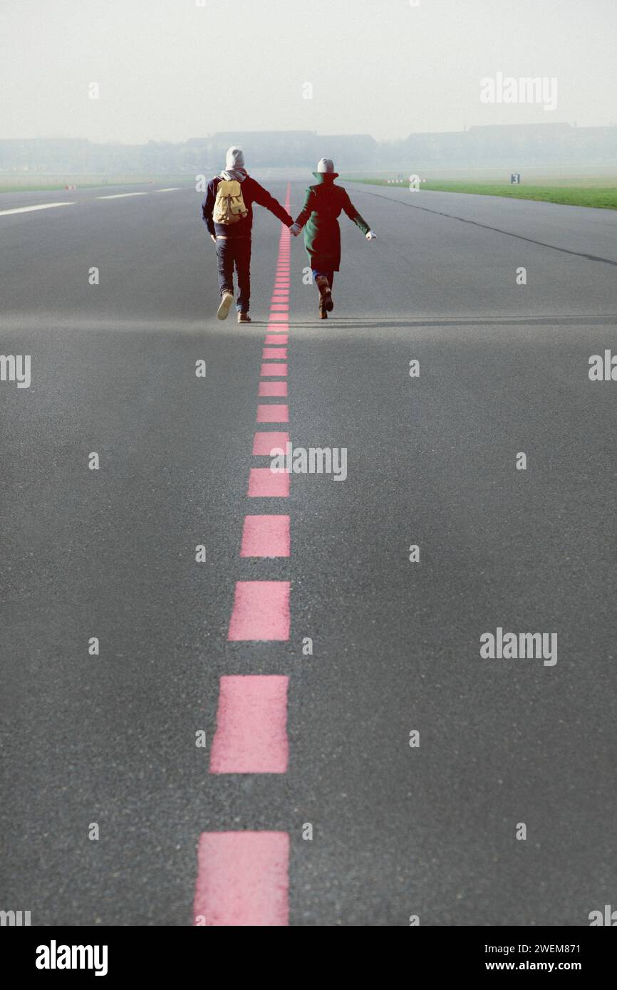 Couple Running along Airport Runway Holding Hands, Rear View Stock ...