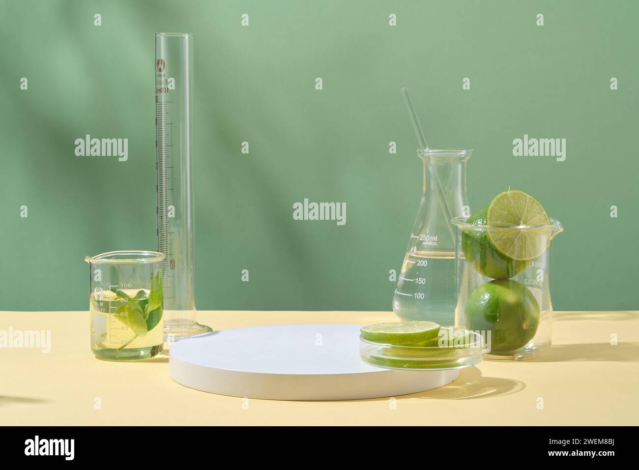 Front view of fresh limes with lab glassware on green background. Empty space for display ...
