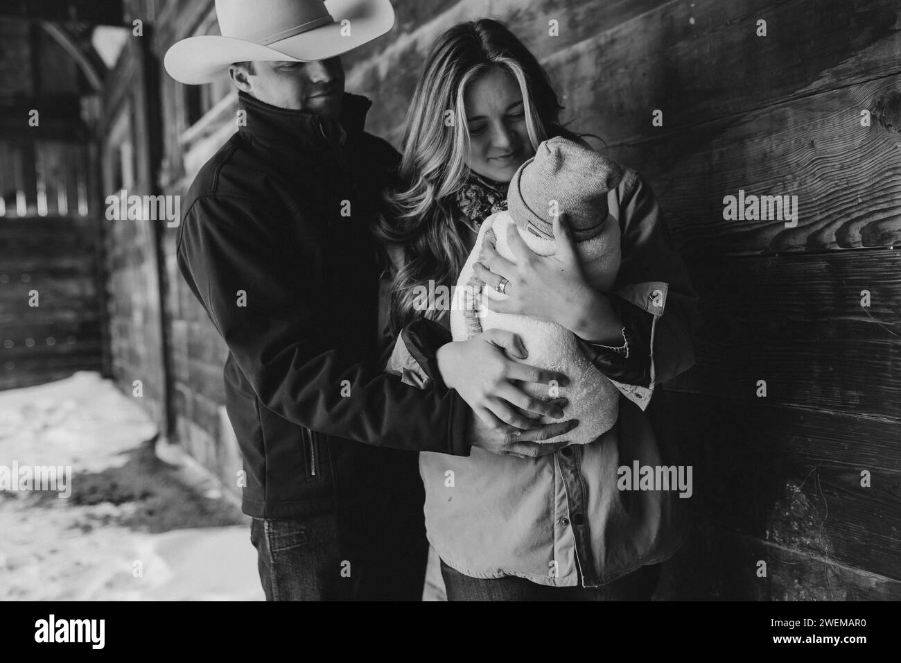Mom and dad in cowboy hat cuddle baby boy by the horse barn Stock Photo ...