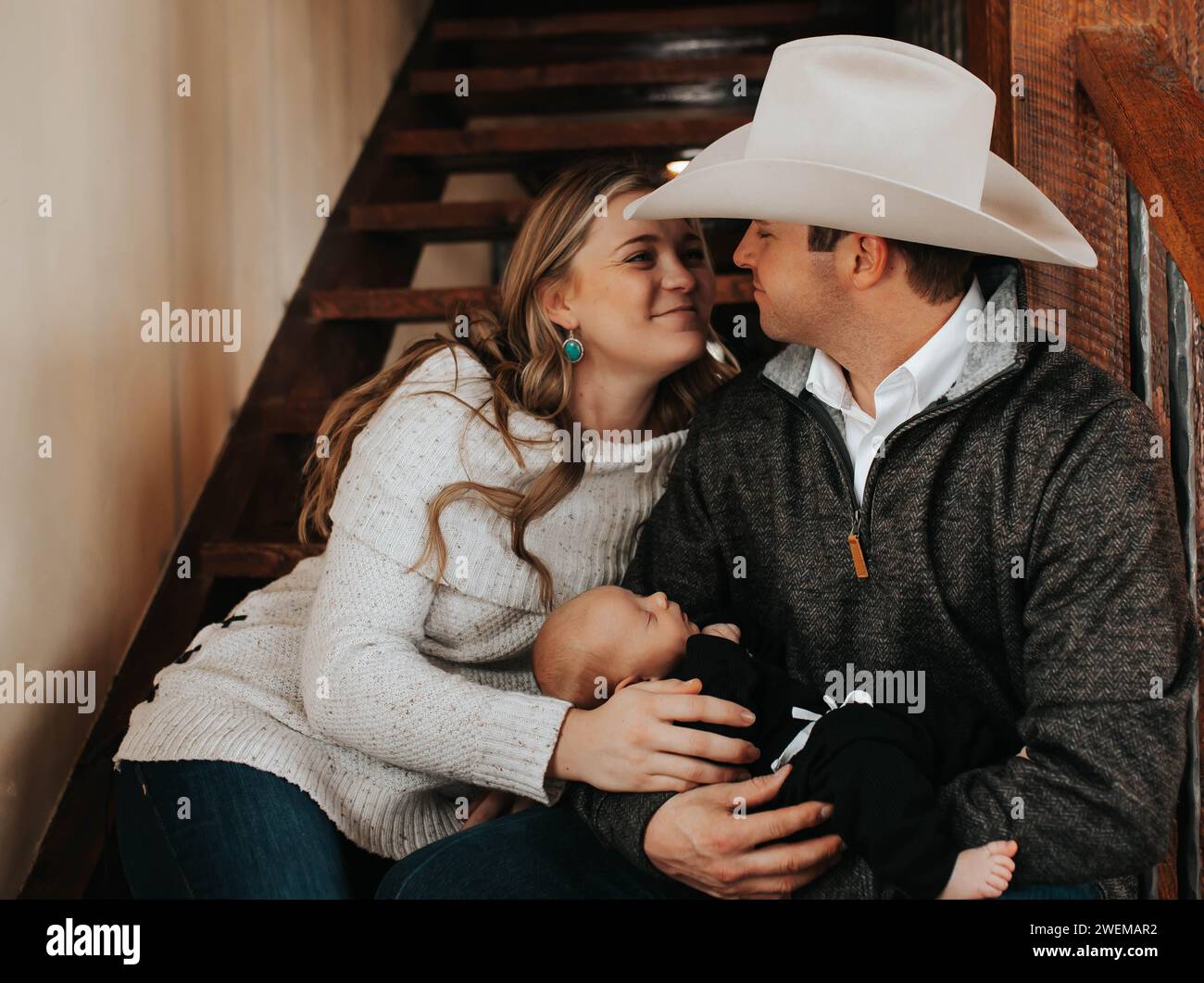 Mom and dad cuddle their new baby boy on wooden stairs Stock Photo - Alamy