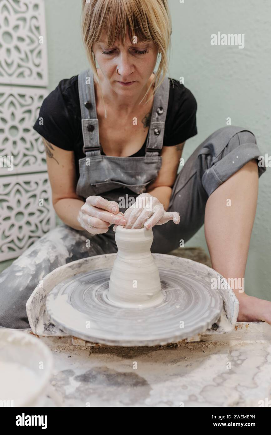 Woman sits at pottery wheel while throwing pots in home studio Stock ...