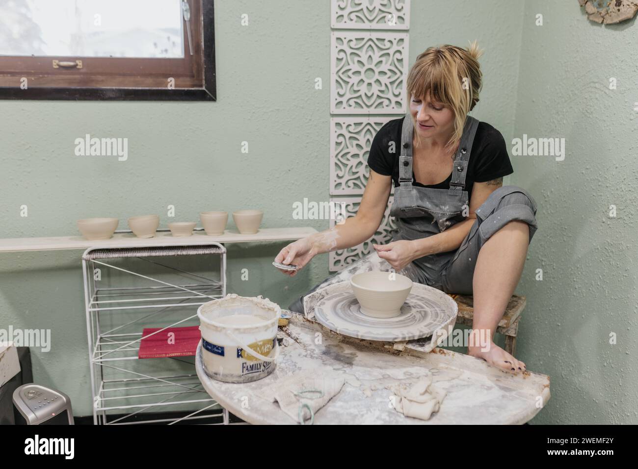 Woman sits at pottery wheel while throwing pots in home studio Stock ...