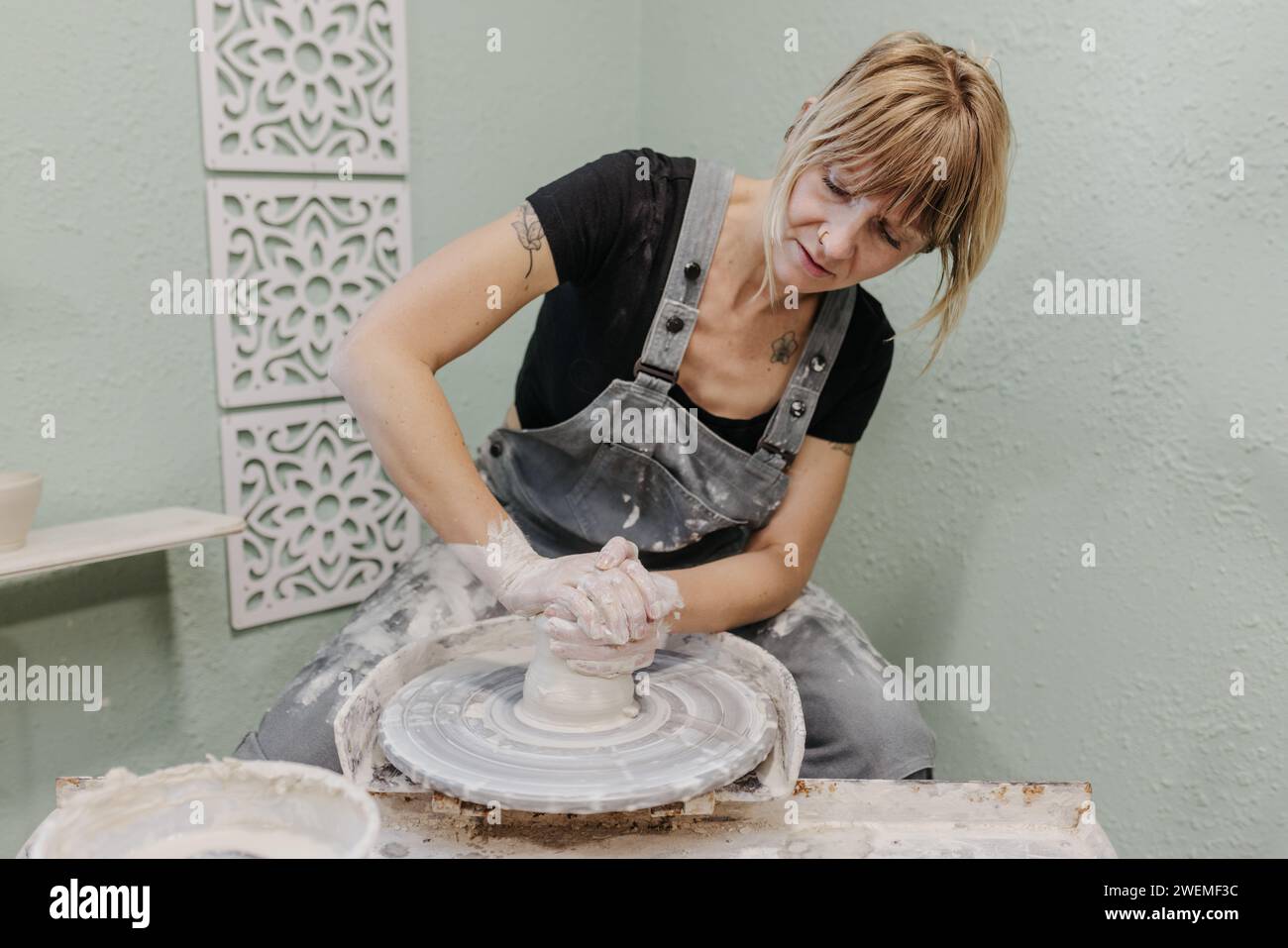 Woman sits at pottery wheel while throwing pots in home studio Stock ...