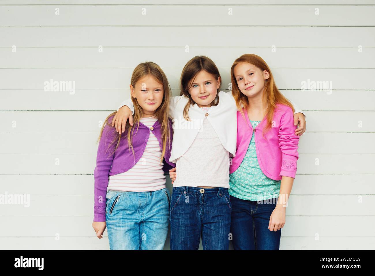 Group of 3 little girls standing outdoors against white wooden ...