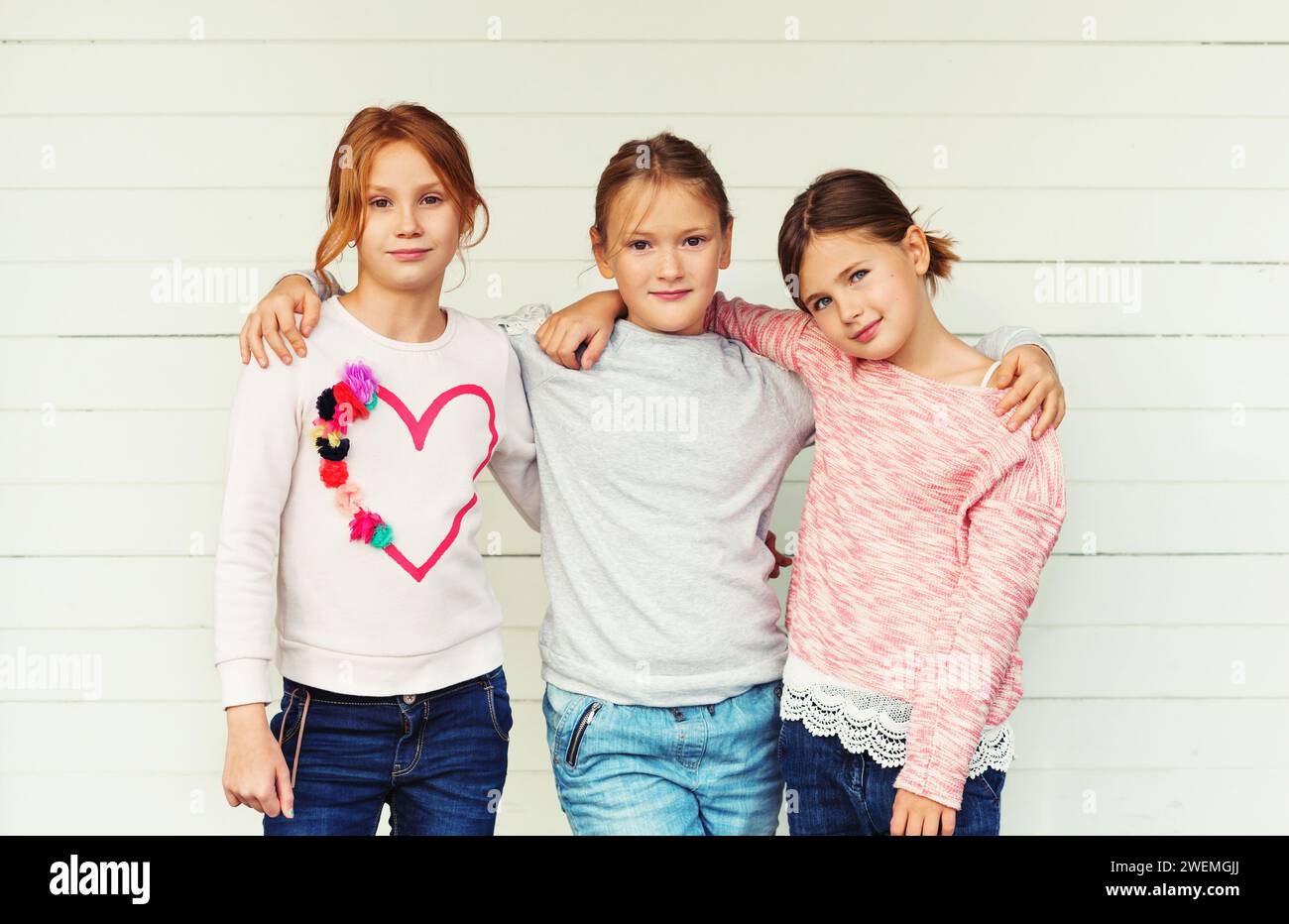 Group of 3 little girls standing outdoors against white wooden ...