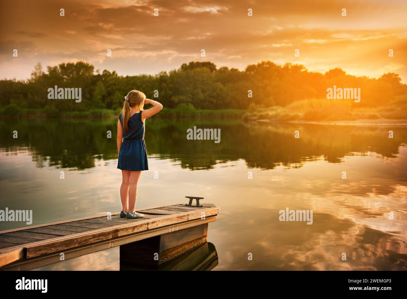Cute little girl enjoying gorgeous sunset at the pier by the lake ...