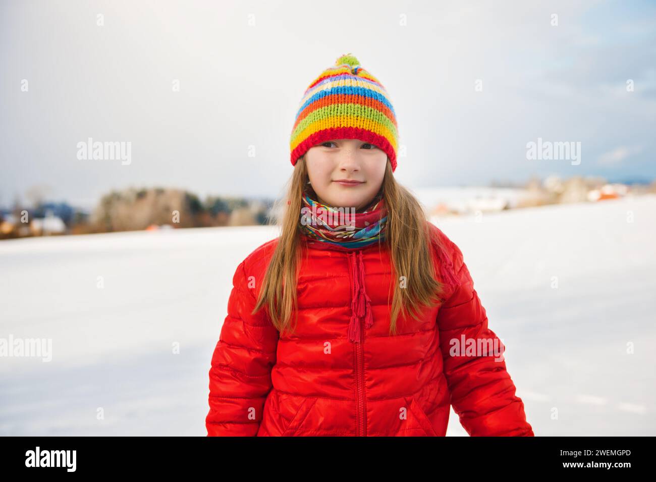 Little girl wearing red jacket and colorful hat, playing with snow in ...
