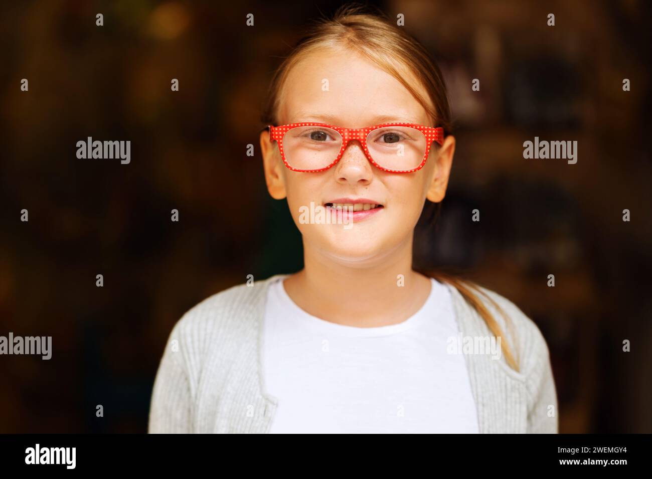 Portrait of a cute little girl in red polka dot glasses against dark ...