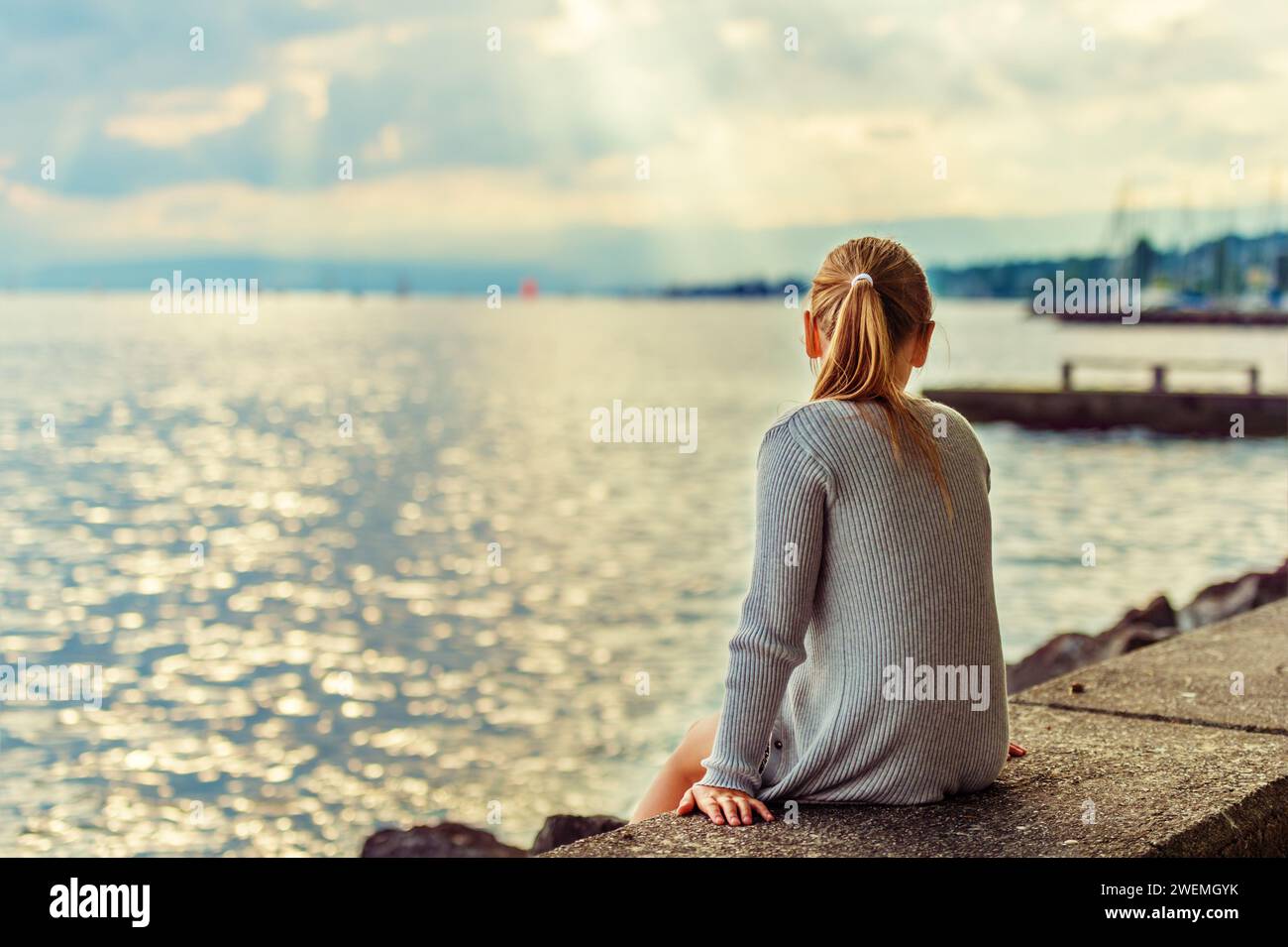 Cute little girl resting by the lake, admiring amazing sunset, rays of ...