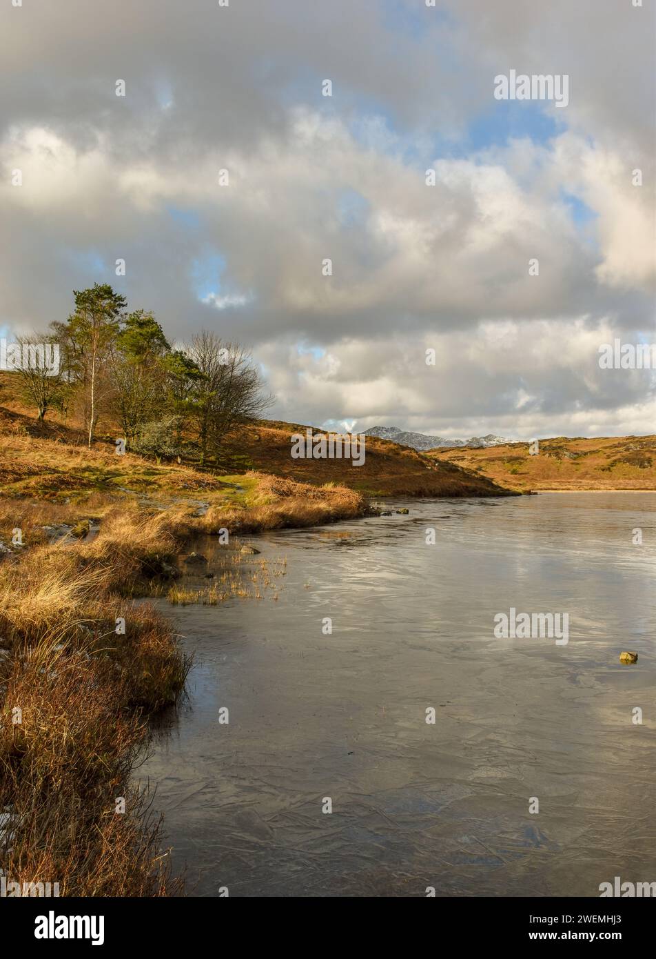 The icy water of Beacon tarn and it's banks in winter beneath a patchy ...