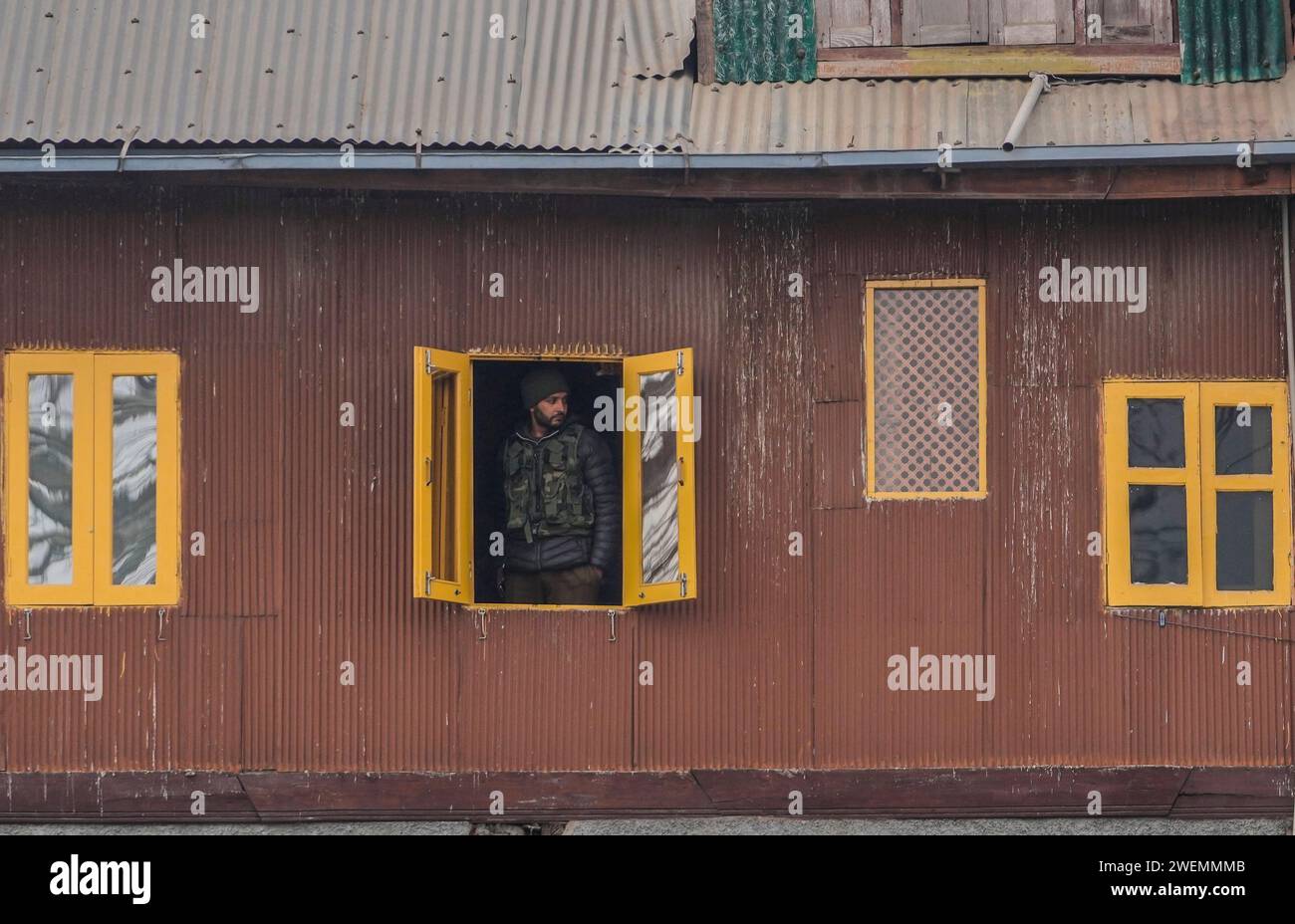 An Indian policeman stands guard on the window of residential houses ...