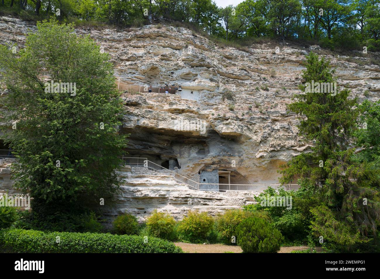 View of cave dwellings in a large rock face surrounded by trees and ...