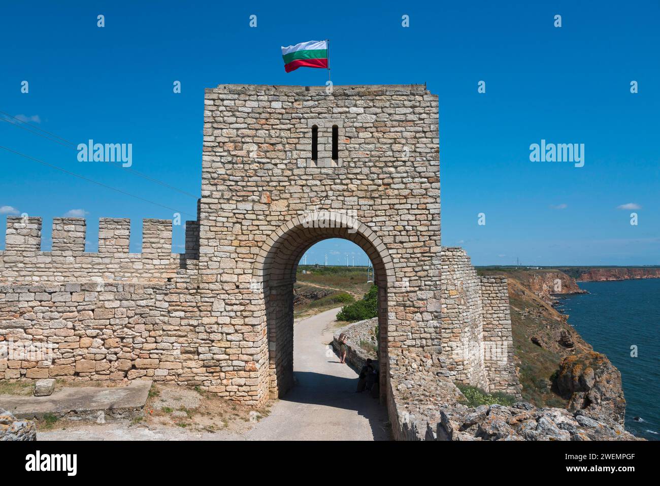 Stone archway of an old fortress with waving flag next to a steep cliff ...