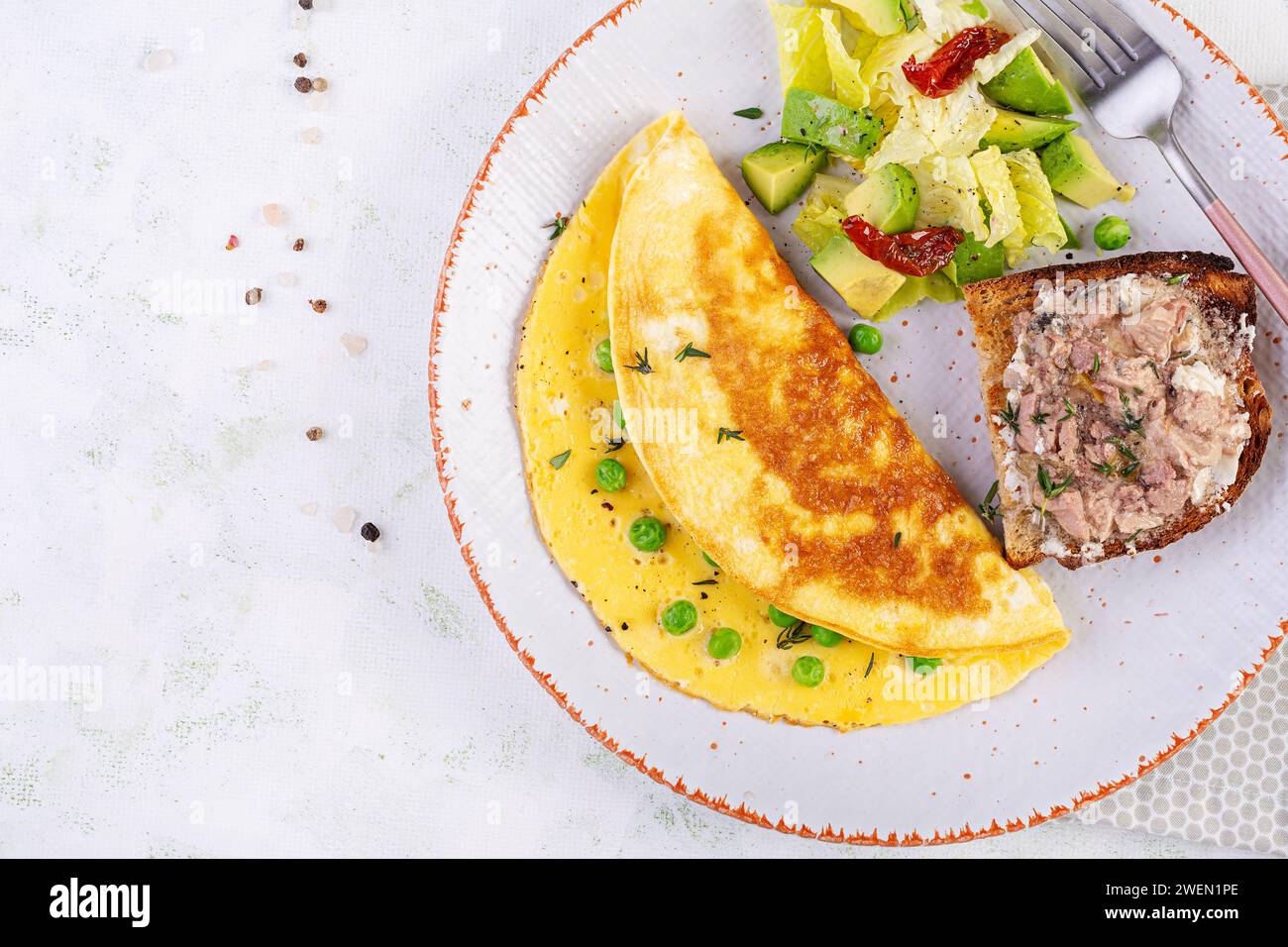 Omelette with green peas and toast with cod liver on white plate ...