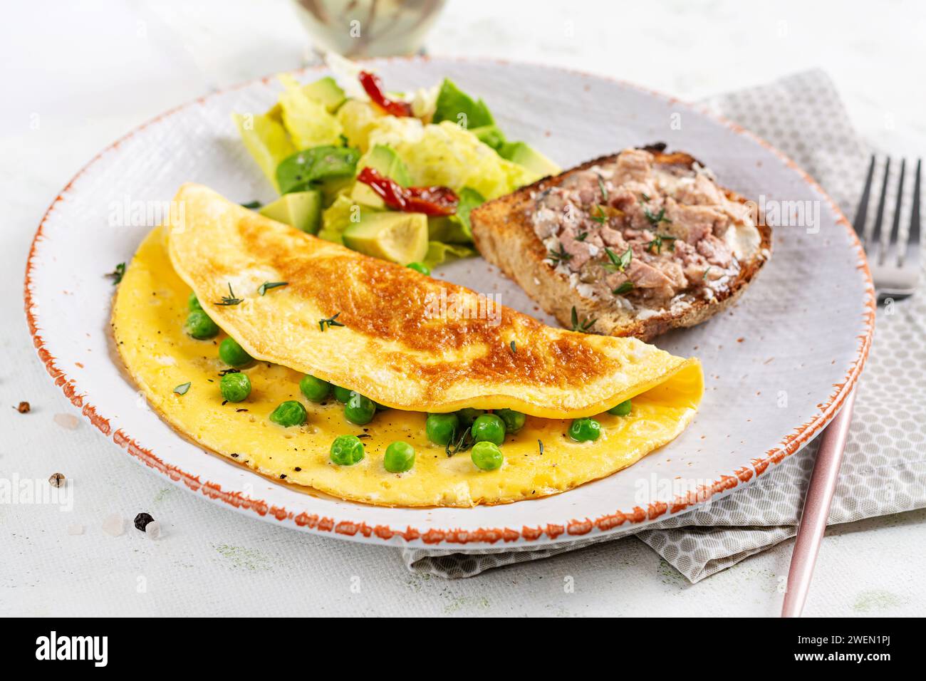 Omelette with green peas and toast with cod liver on white plate ...