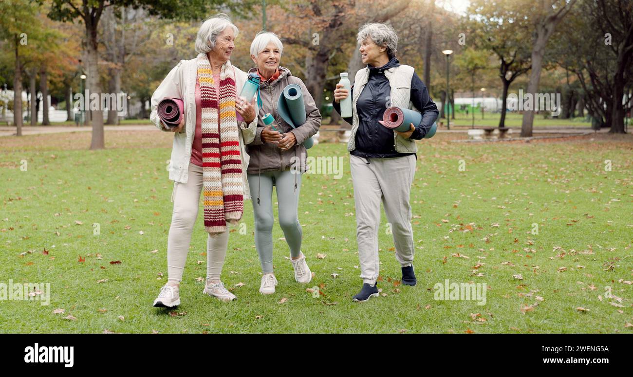 Senior friends, walking and talking with yoga mats in the park to relax ...