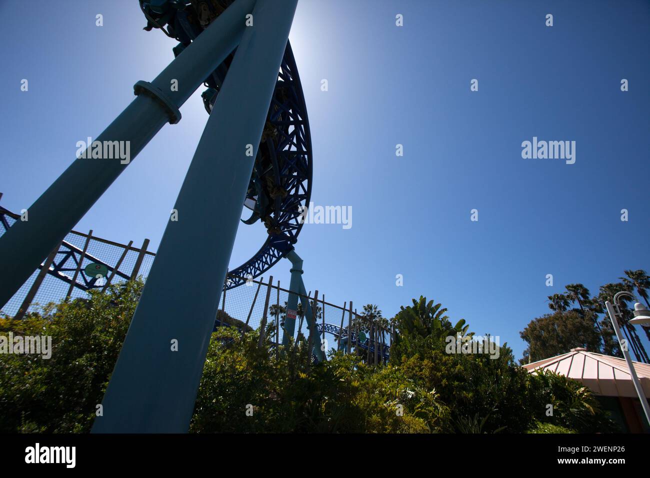 A rollercoaster inverts overhead against a blue sky in a theme park ...