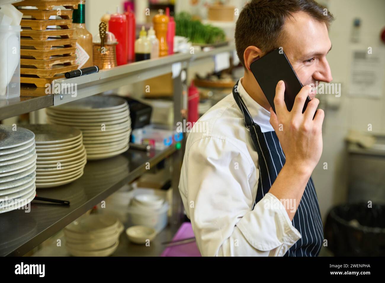 Cook in a chefs apron communicates on his mobile phone Stock Photo - Alamy