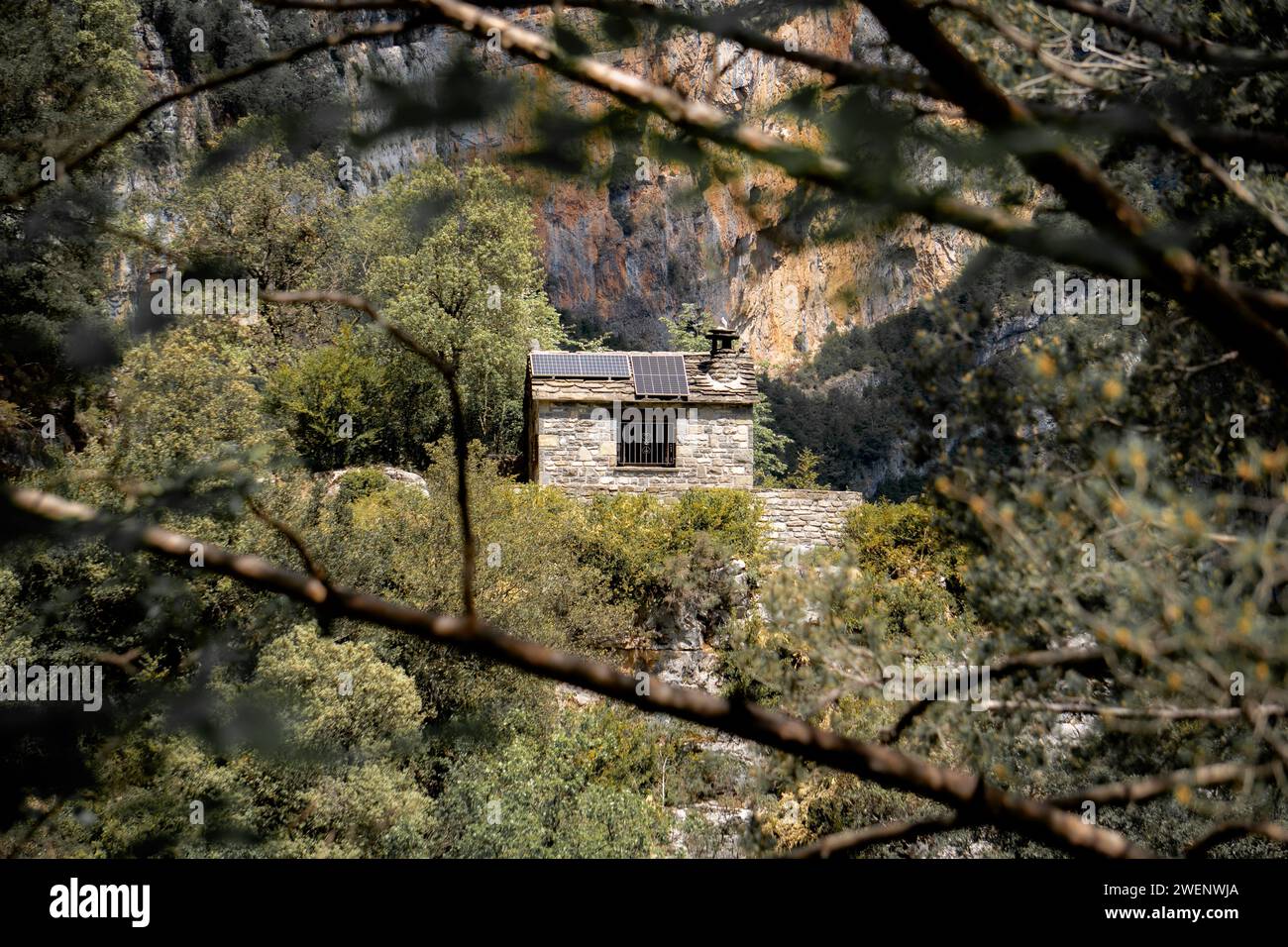 Small stone house in a mountain gorge seen through leaves, with ...