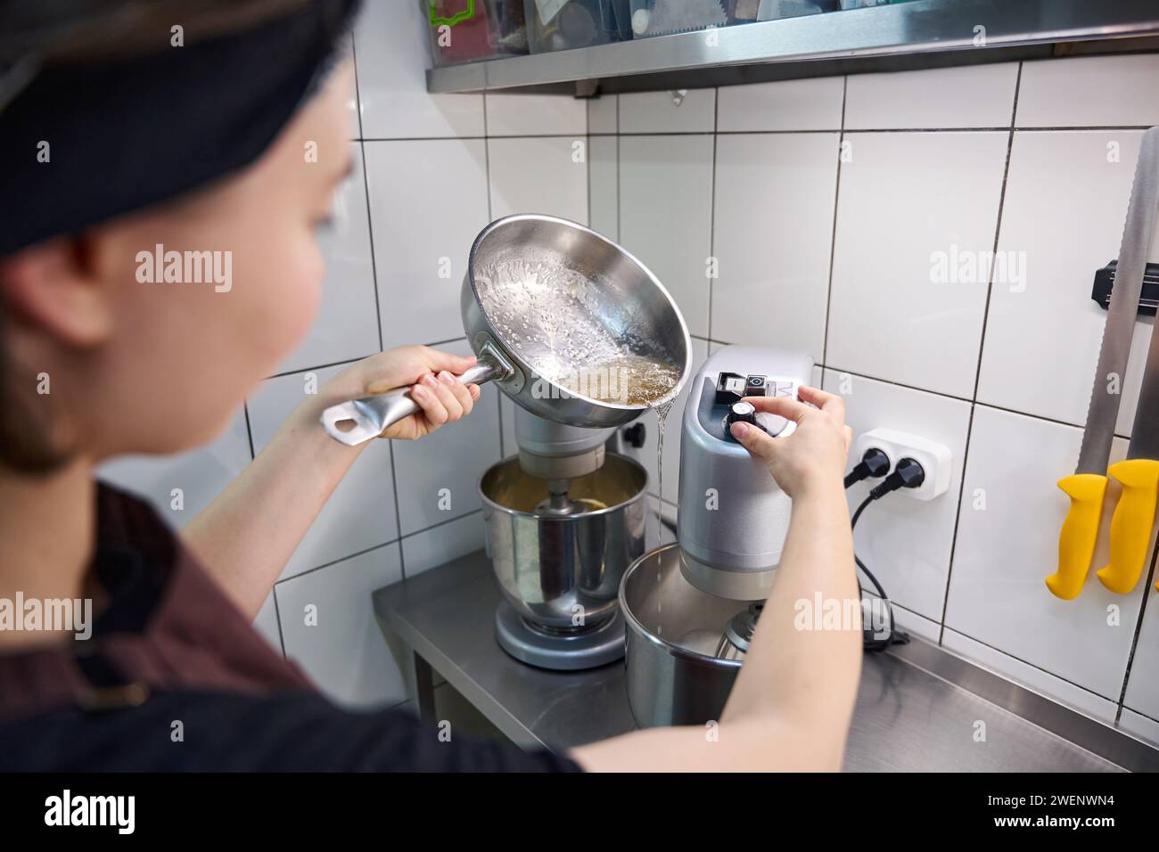 Qualified pastry chef adding confectionery ingredients to stand mixer ...