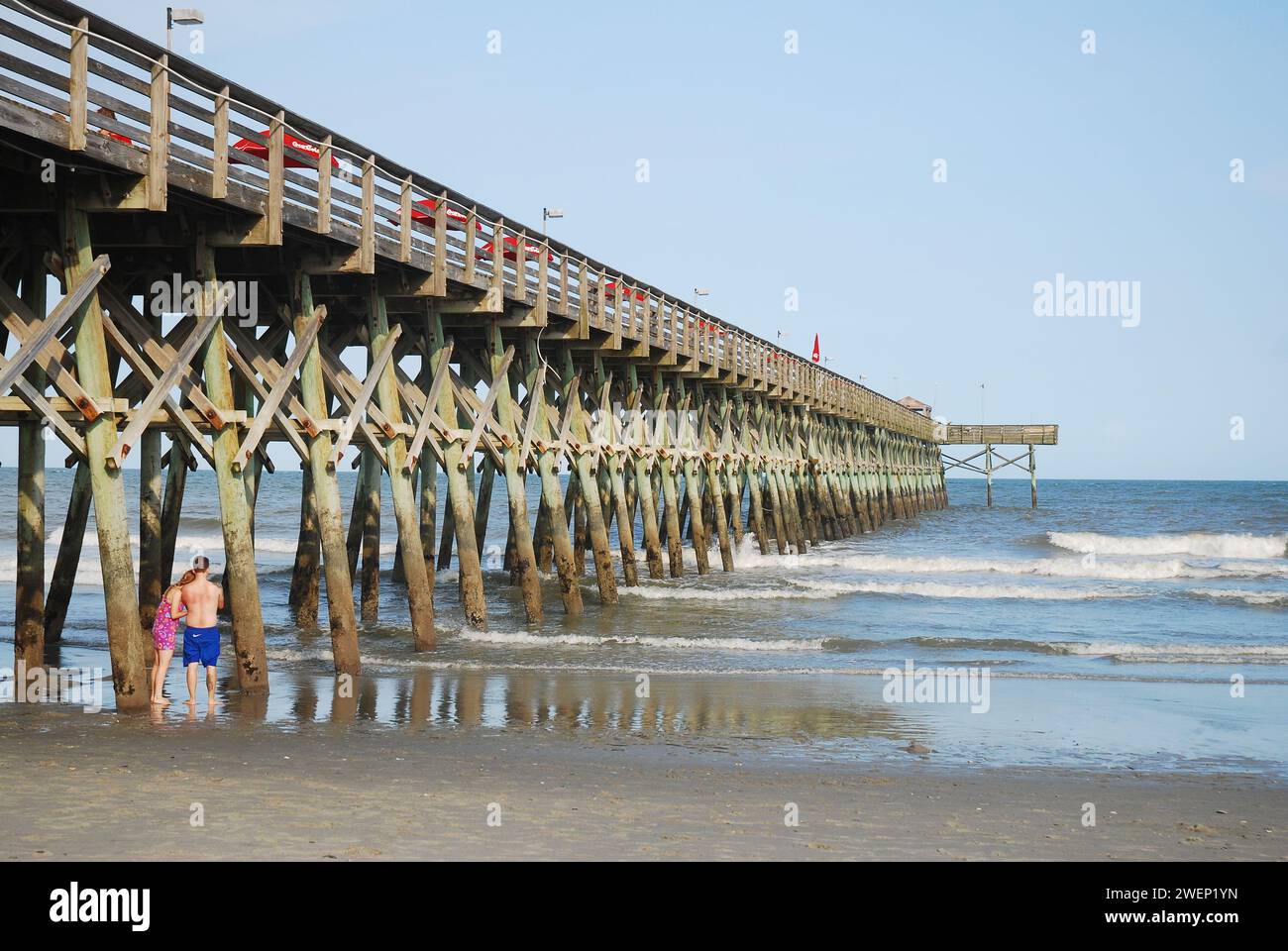 A couple stands under the Second Avenue Pier as the waves roll in from ...