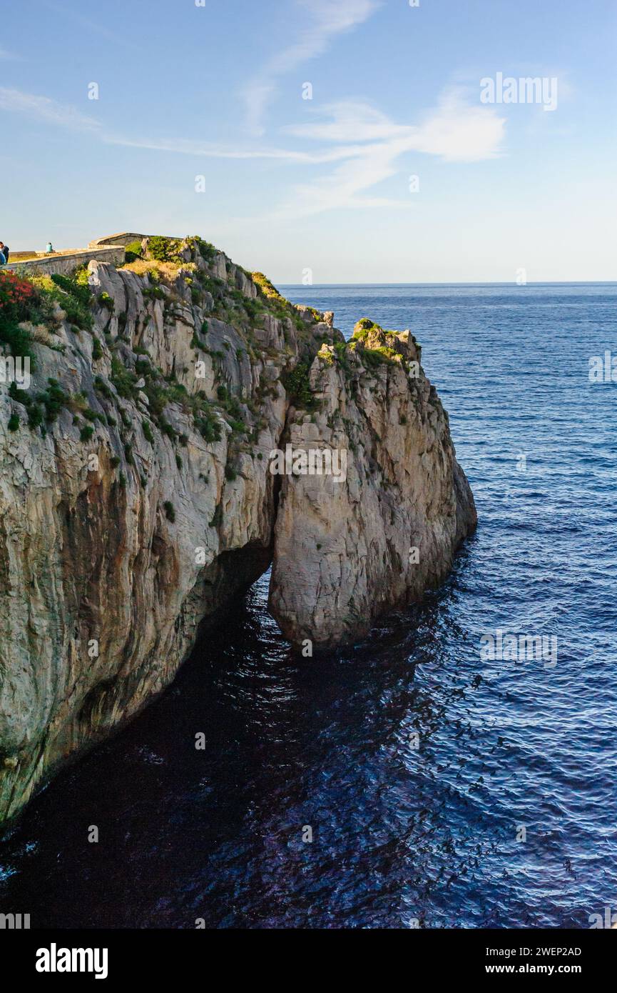 A natural limestone cliff majestically towers over the serene blue sea ...