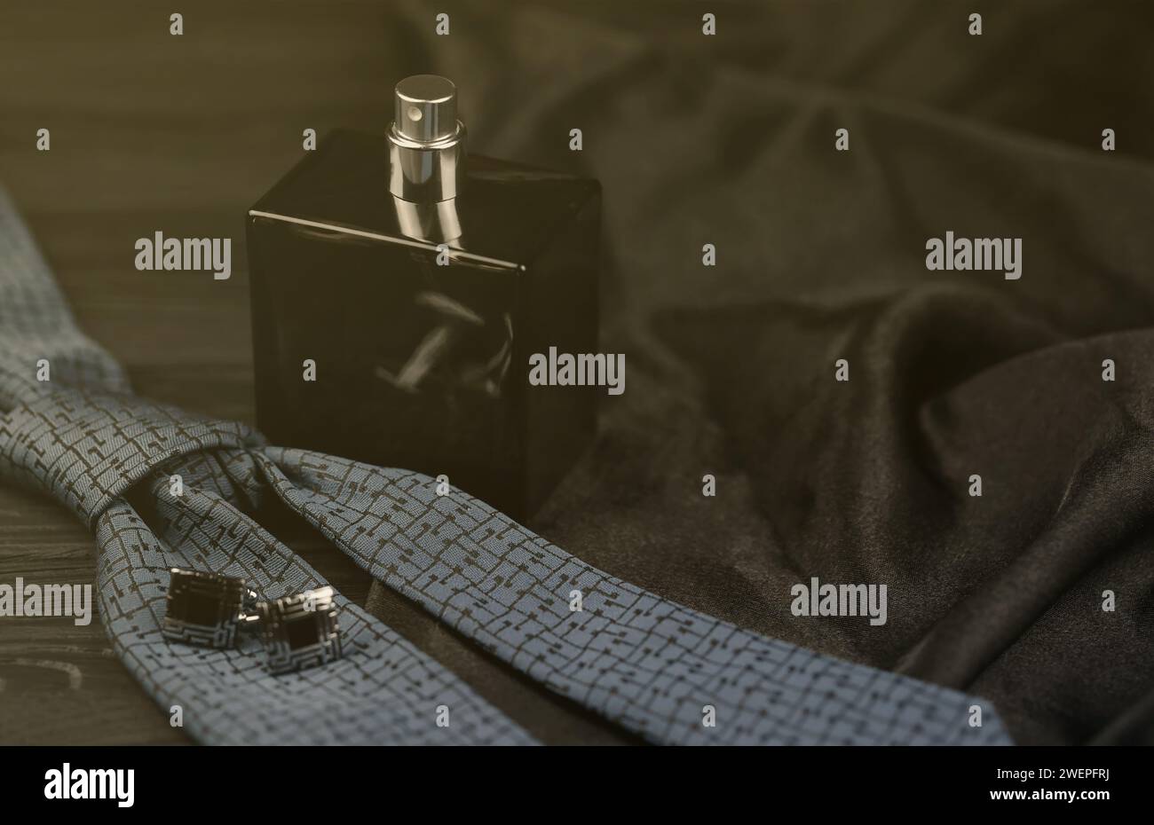 A bottle of mens cologne and cufflinks with blue tie lie on a black ...