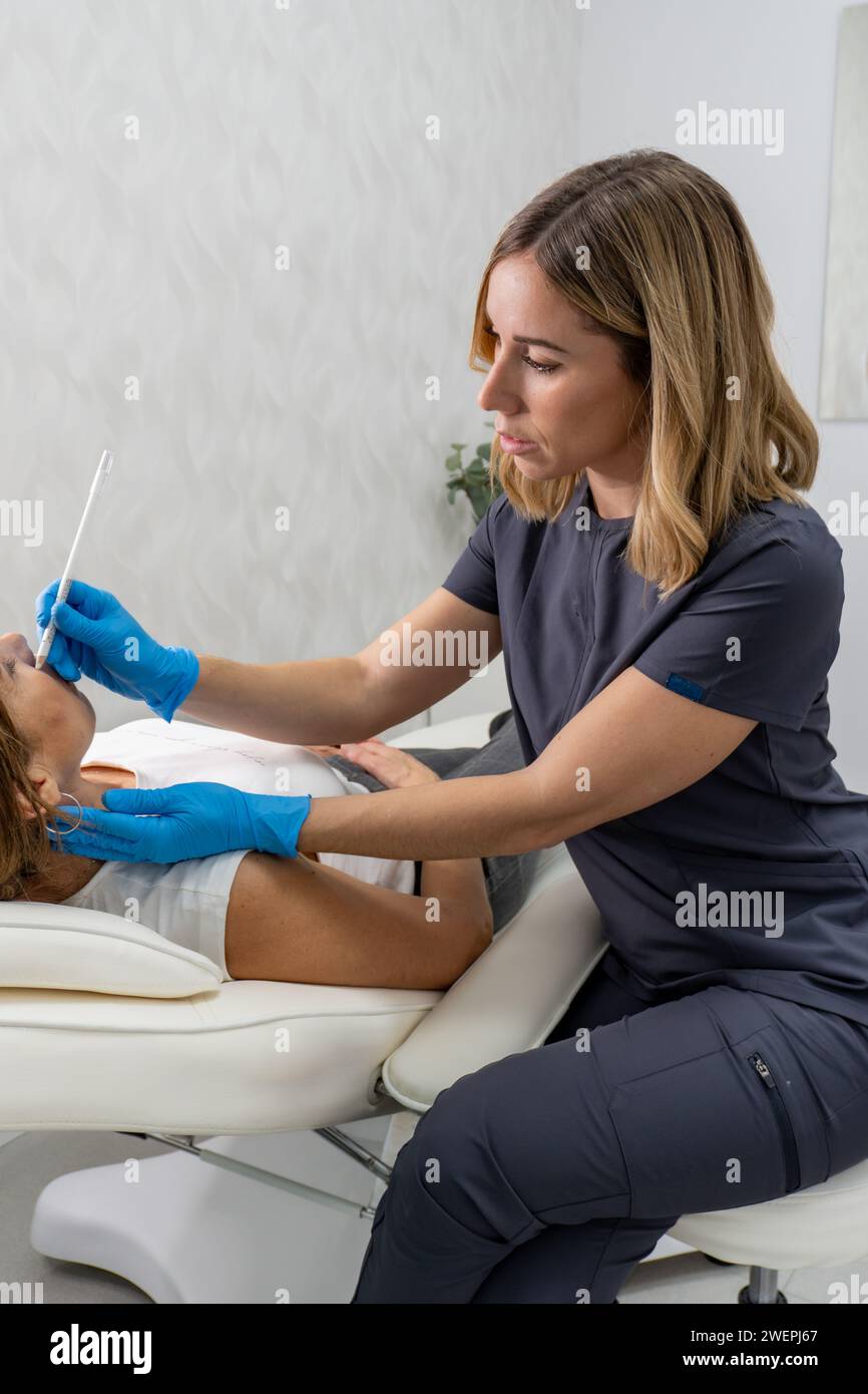 young esthetician marks with pen at laying client's face at clinic ...