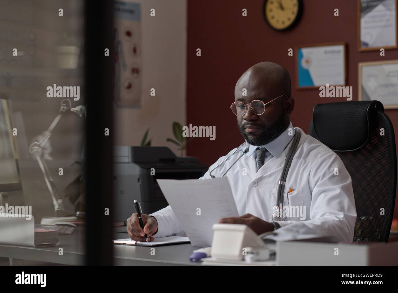 Serious african american doctor in uniform sitting at his desk in ...